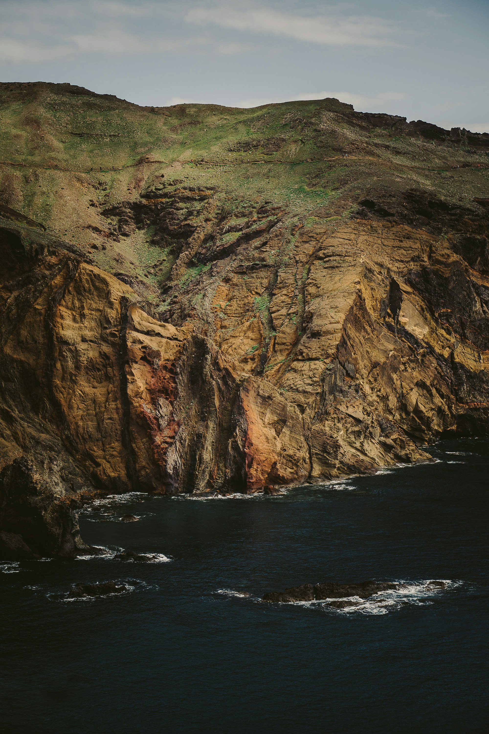 Rugged cliffs meet the deep blue sea under a soft sky.