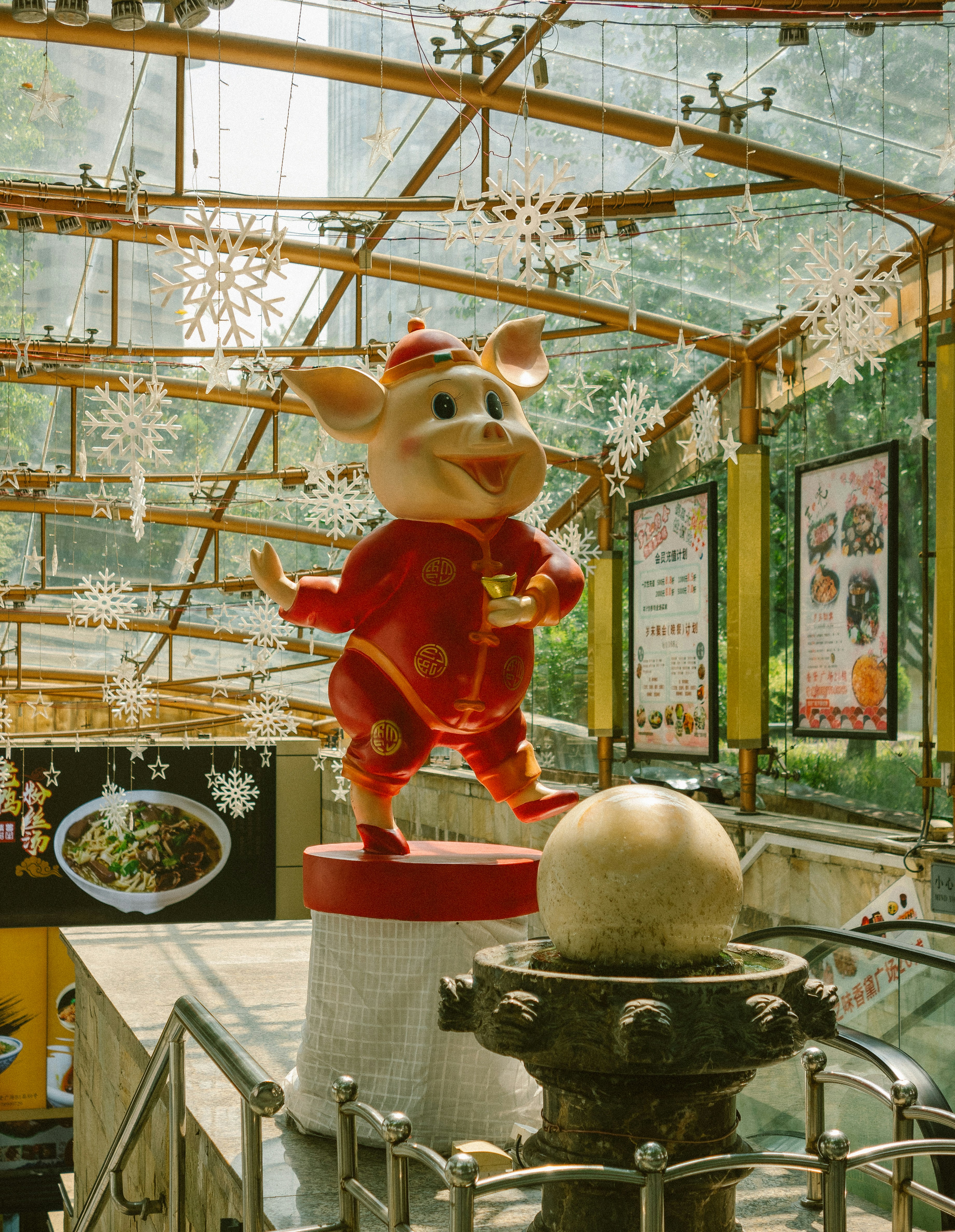 A vibrant pig statue dressed in festive attire stands atop a pedestal, surrounded by decorative snowflakes and restaurant menus in a lively market setting.