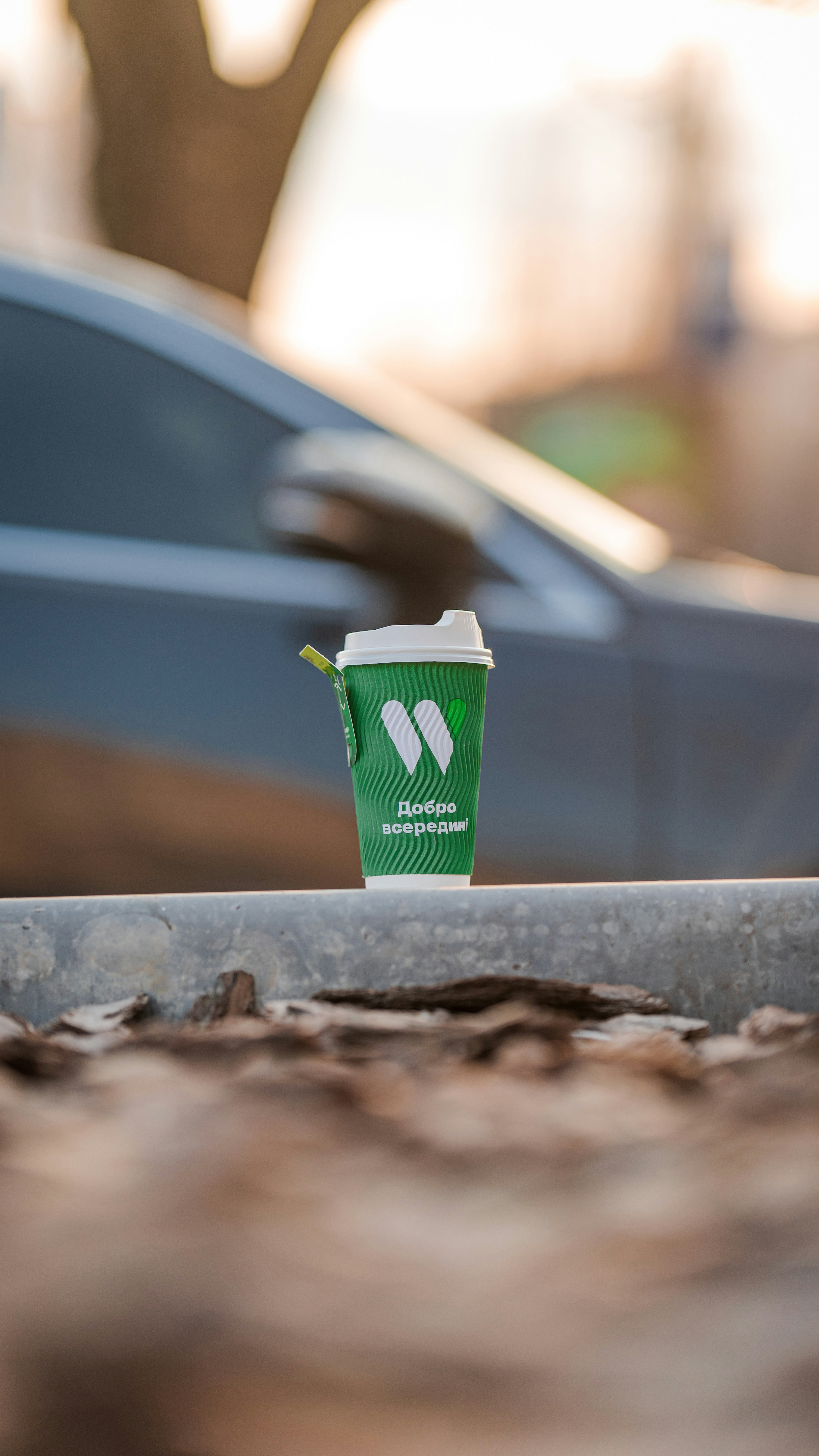 Morning Contour: a lone green cup anchors a quiet curbside scene amid a blurred urban rush