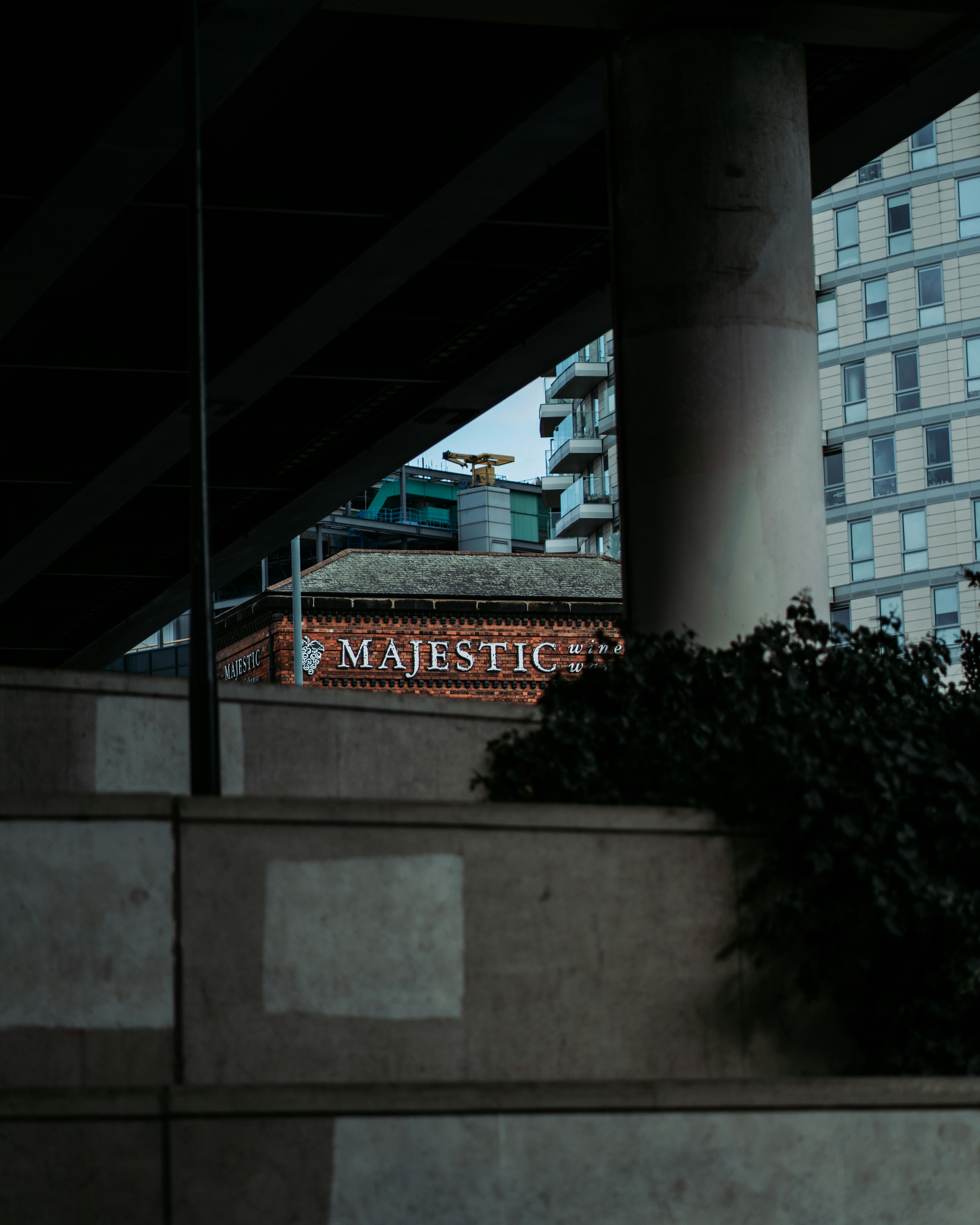 A glimpse of a vintage sign peeking through urban architecture, framed by concrete and greenery.