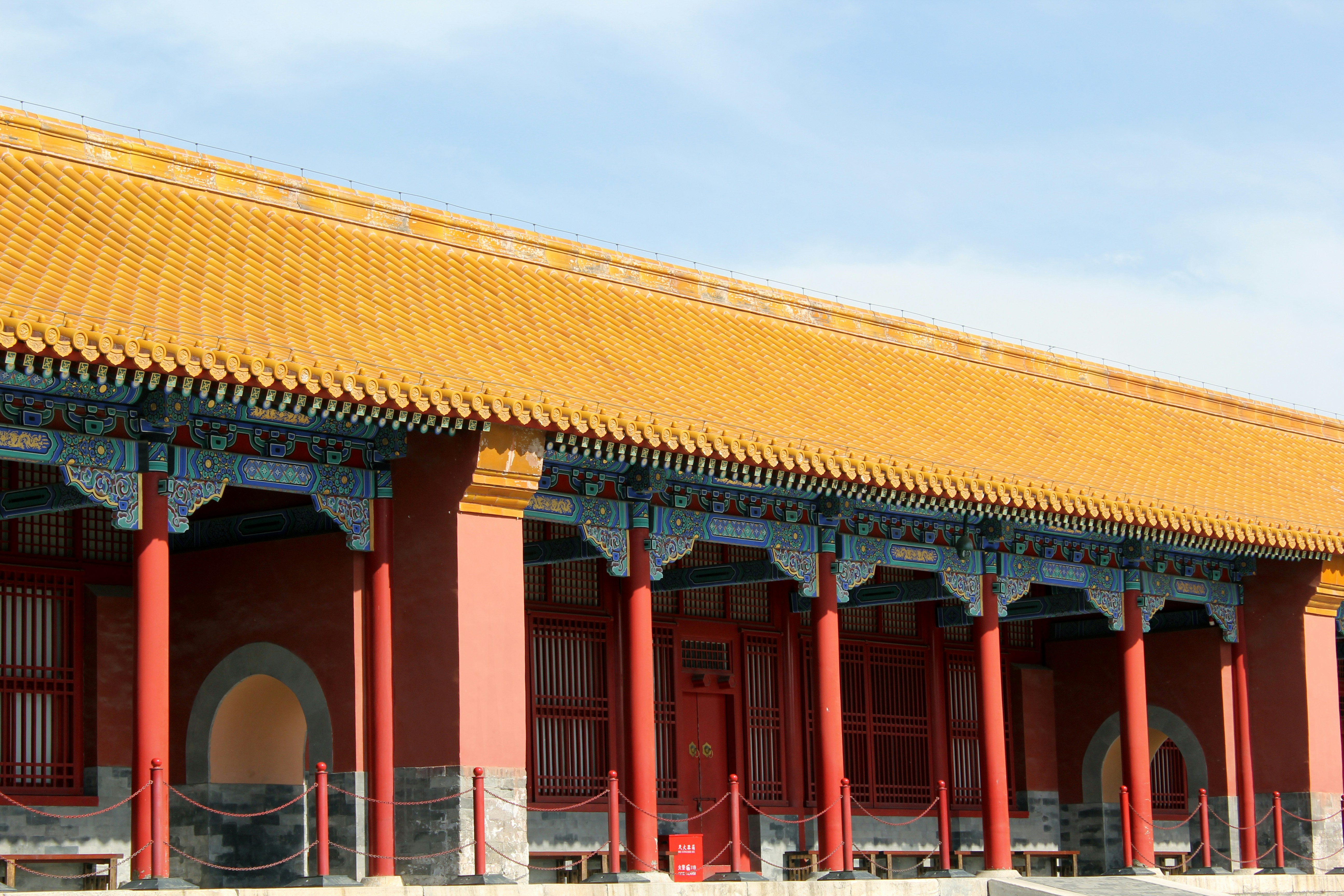 Intricate architectural details of a historical building featuring vibrant red pillars and a striking golden roof under a clear blue sky.