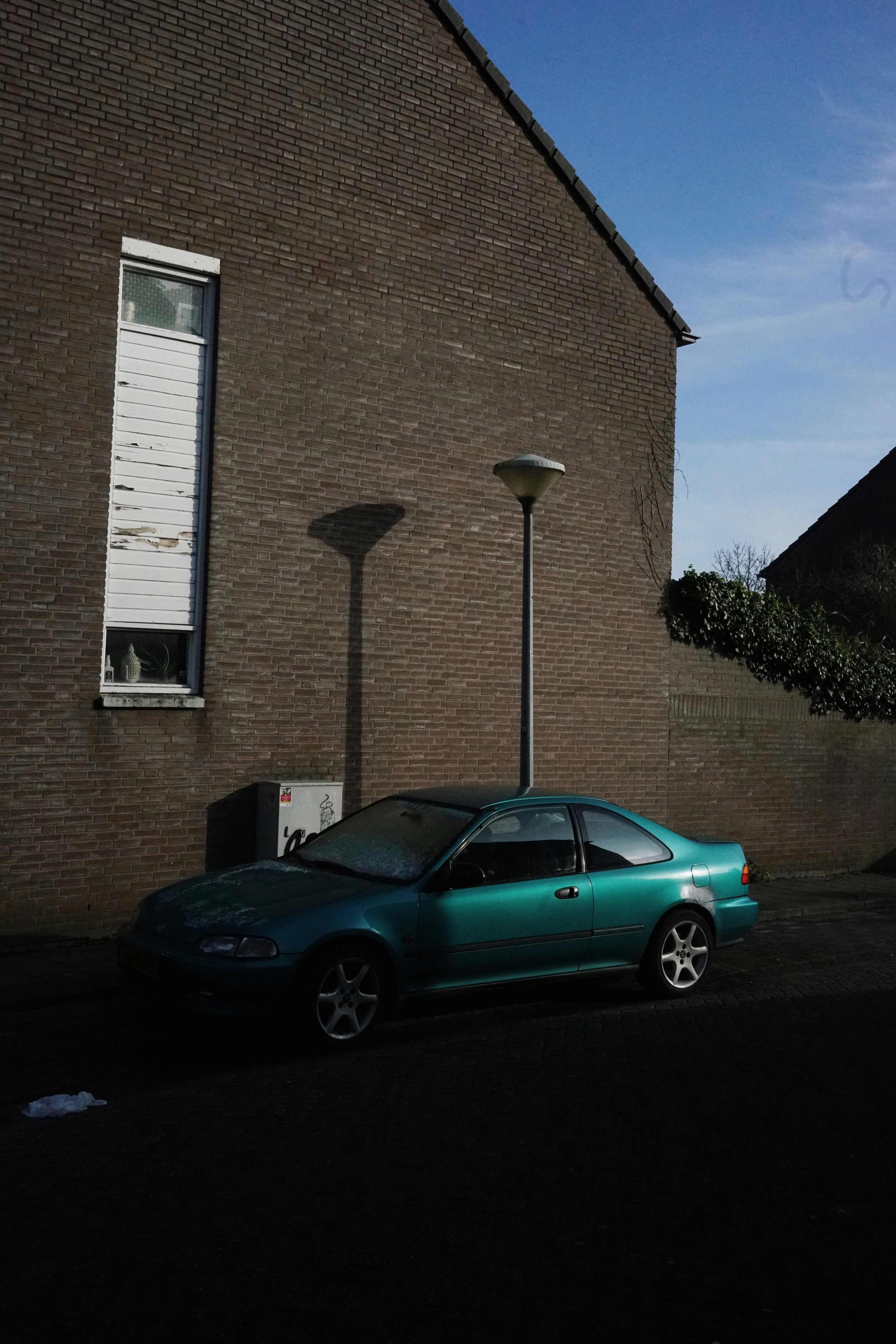 Teal Coupe Beneath a Streetlamp Along a Brick-Walled Street