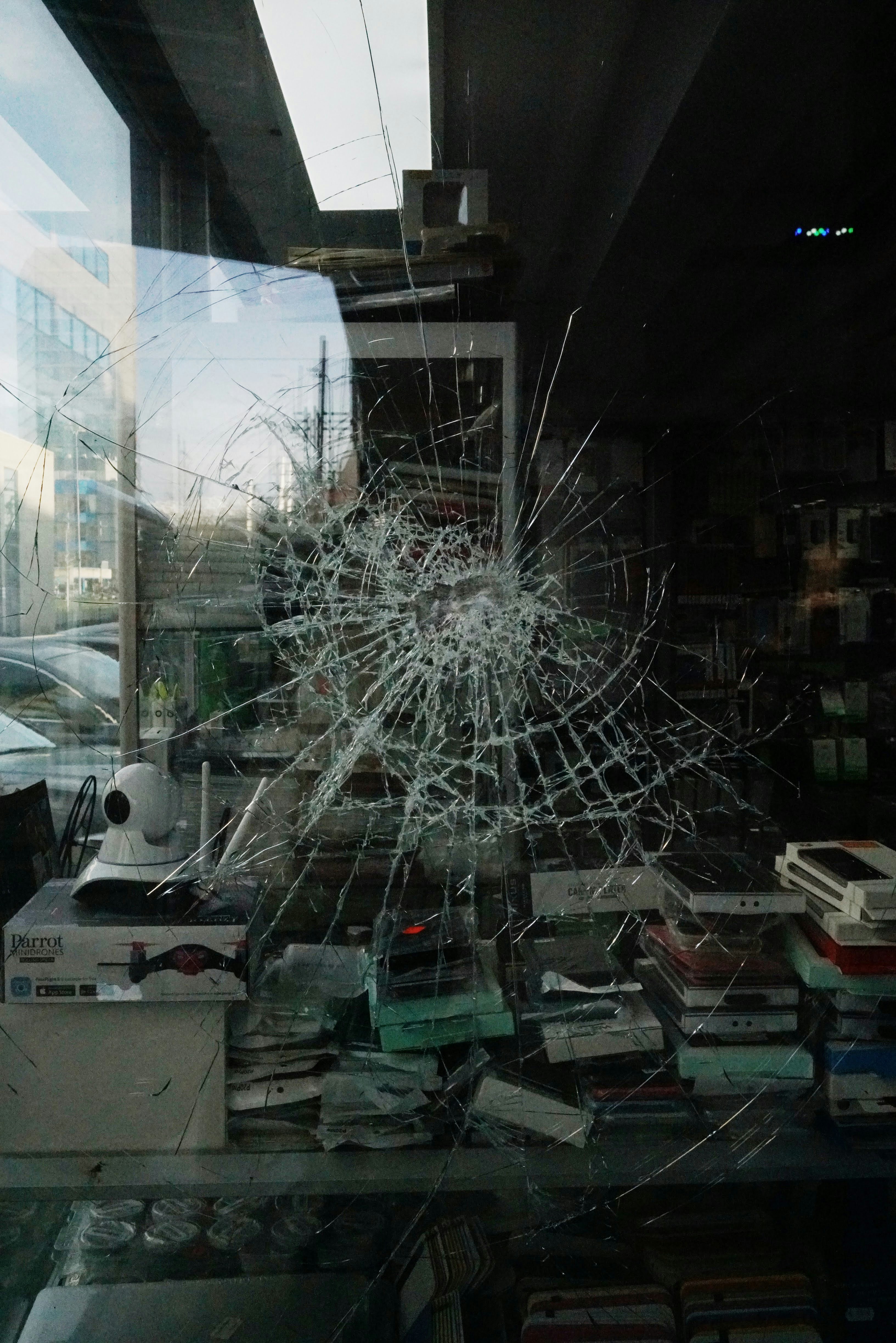 Shattered glass with intricate cracks on a storefront window reflecting the urban landscape.