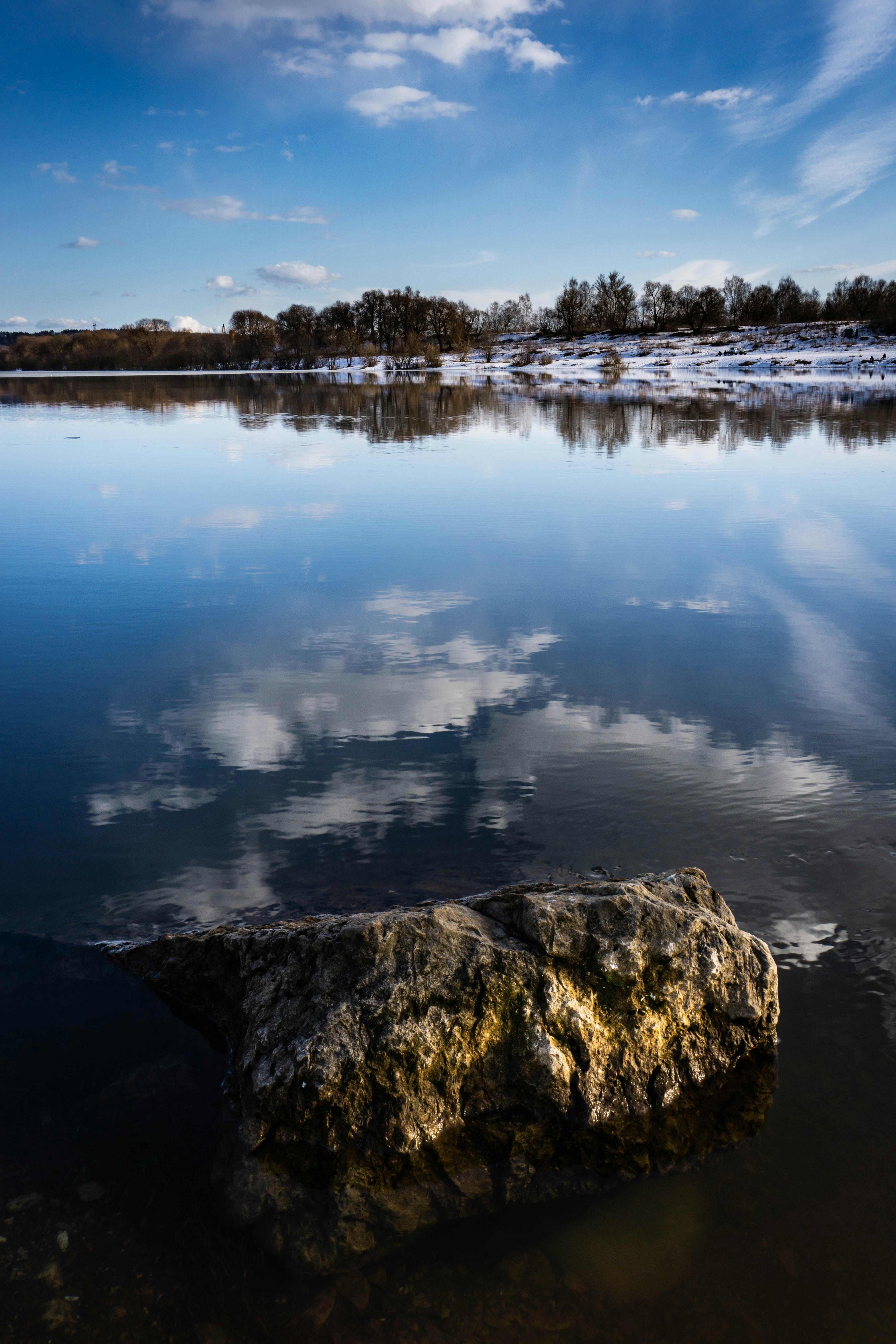 A solitary rock partially submerged in calm water, reflecting a serene sky and surrounding landscape. The tranquil scene captures the essence of nature's balance.