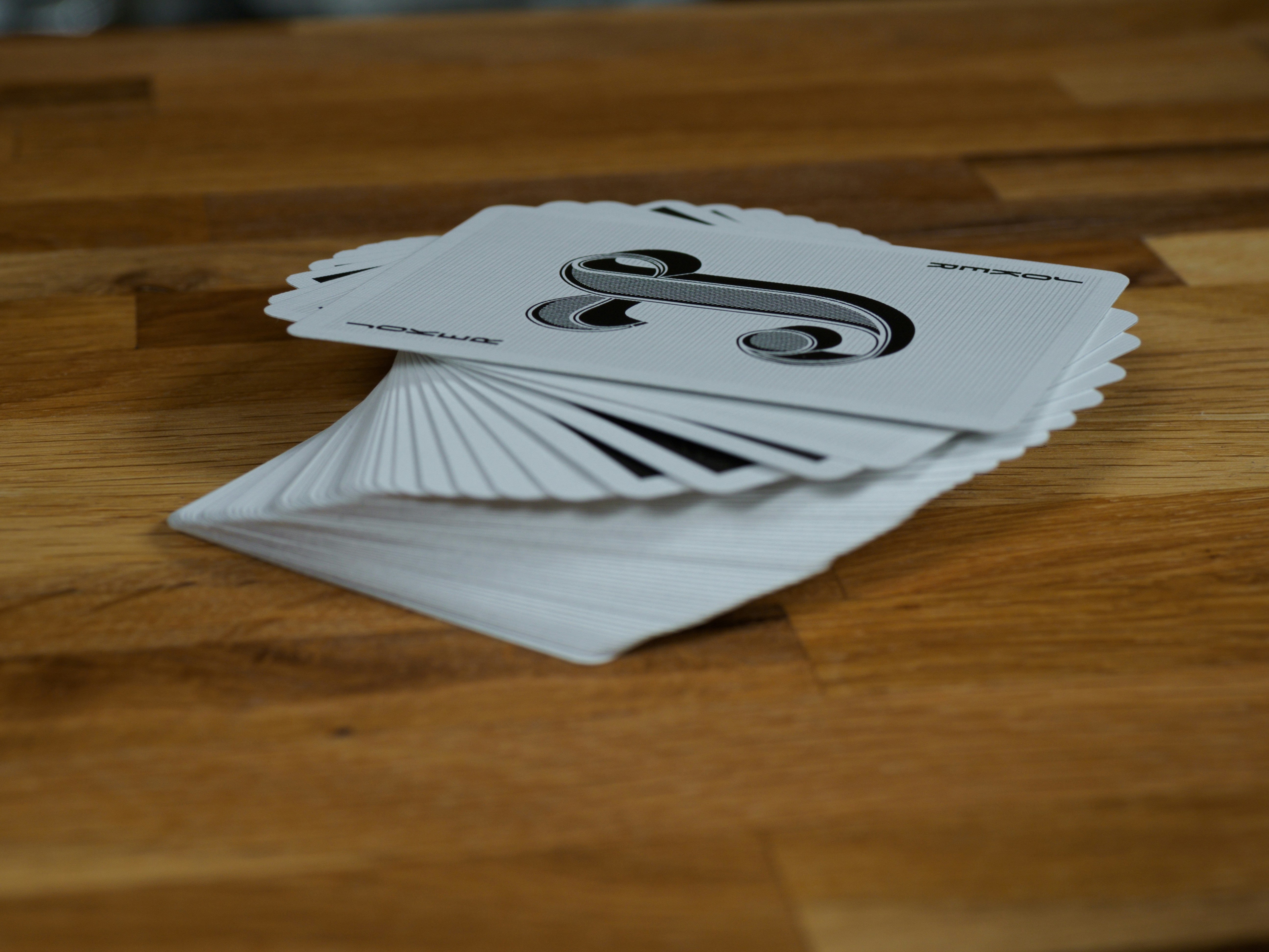 Stack of white playing cards fanned on a warm wooden surface, with bold black illustrations on the top card; minimal depth of field highlights card edges as the focus widens toward the background.