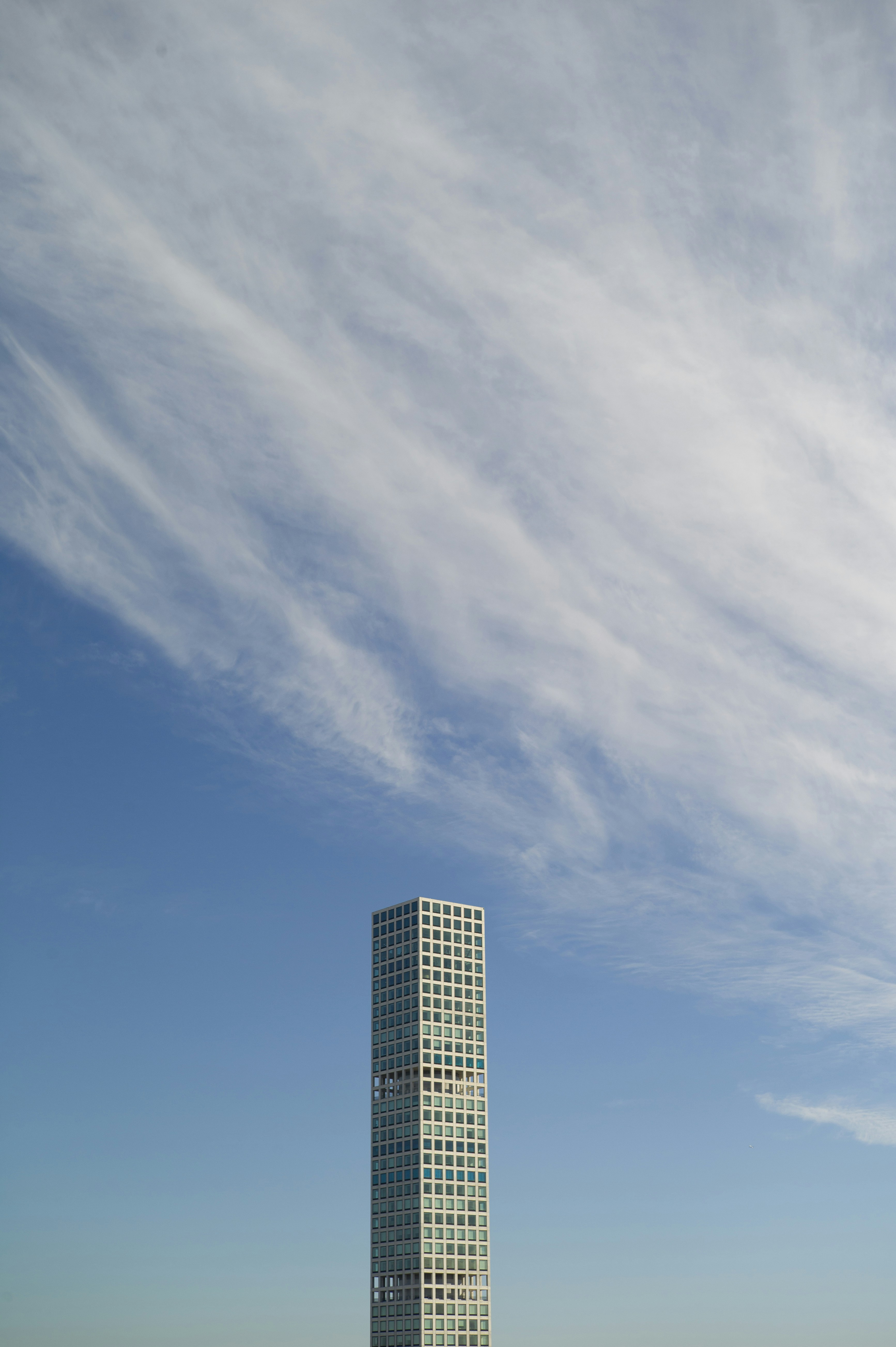 A sleek, modern skyscraper rises against a backdrop of wispy clouds and a clear blue sky.