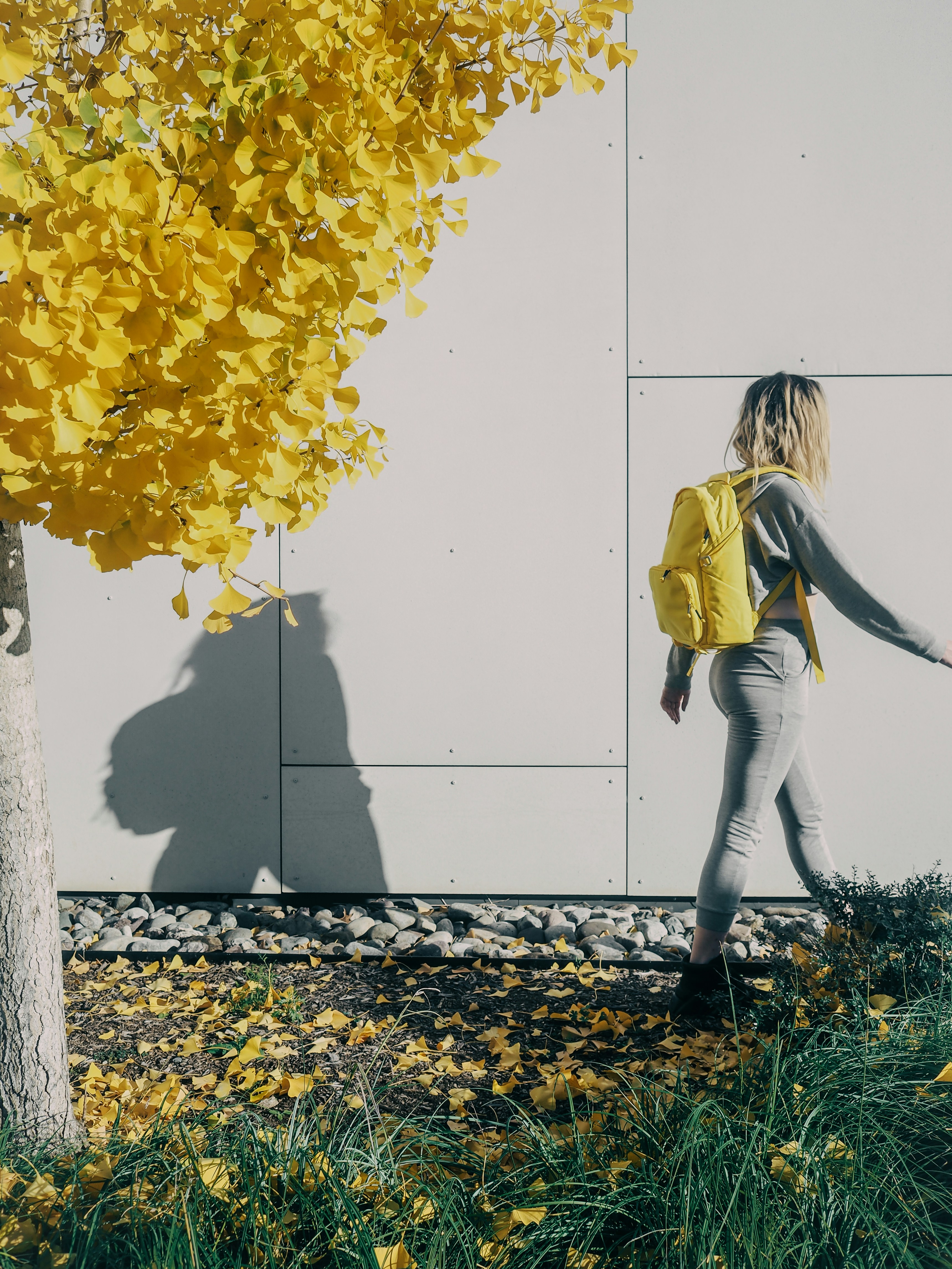 woman in yellow jacket and gray pants standing beside white wall