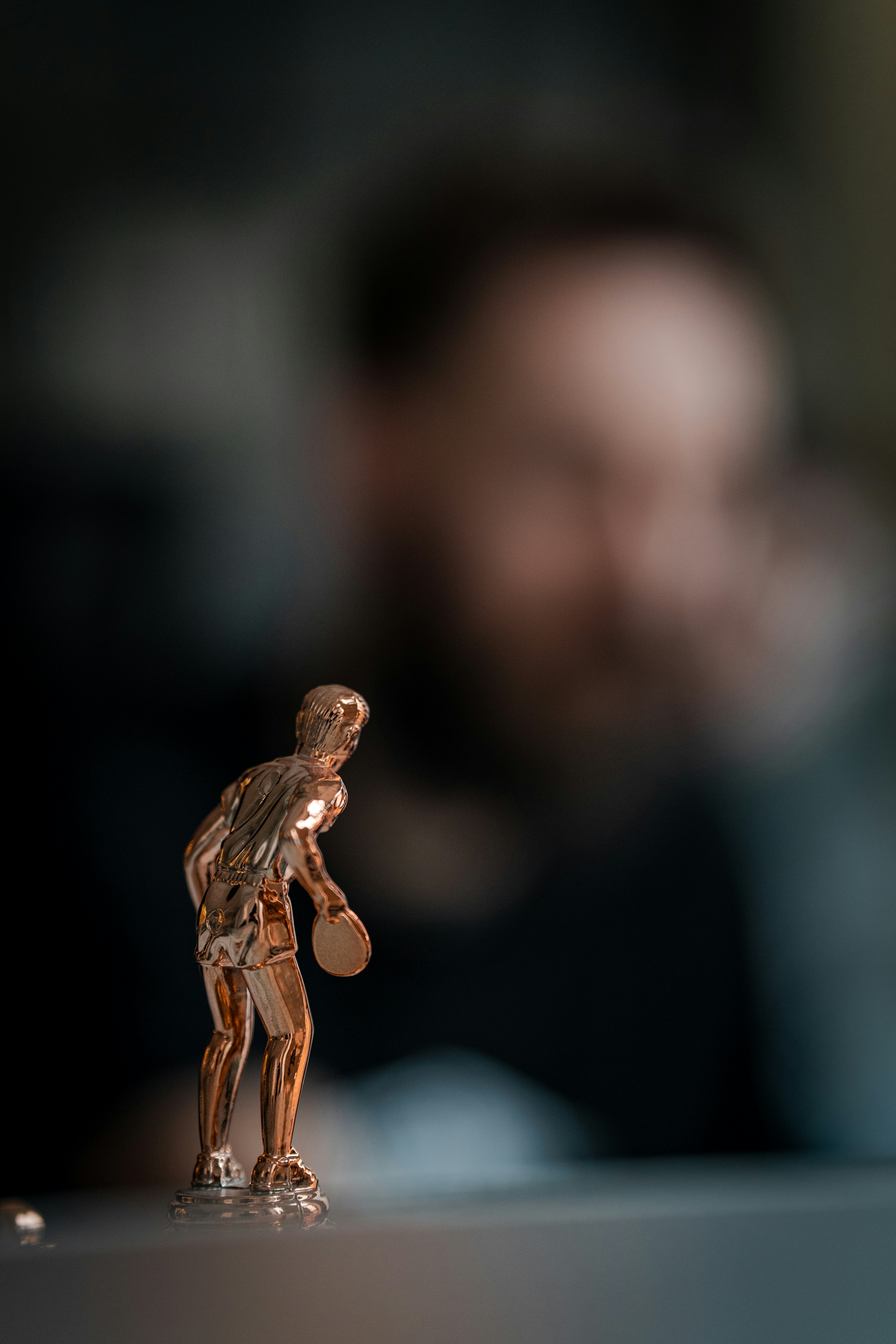 Copper Athlete Figurine on a Glass Surface, with a Soft-Blurred Portrait in the Background