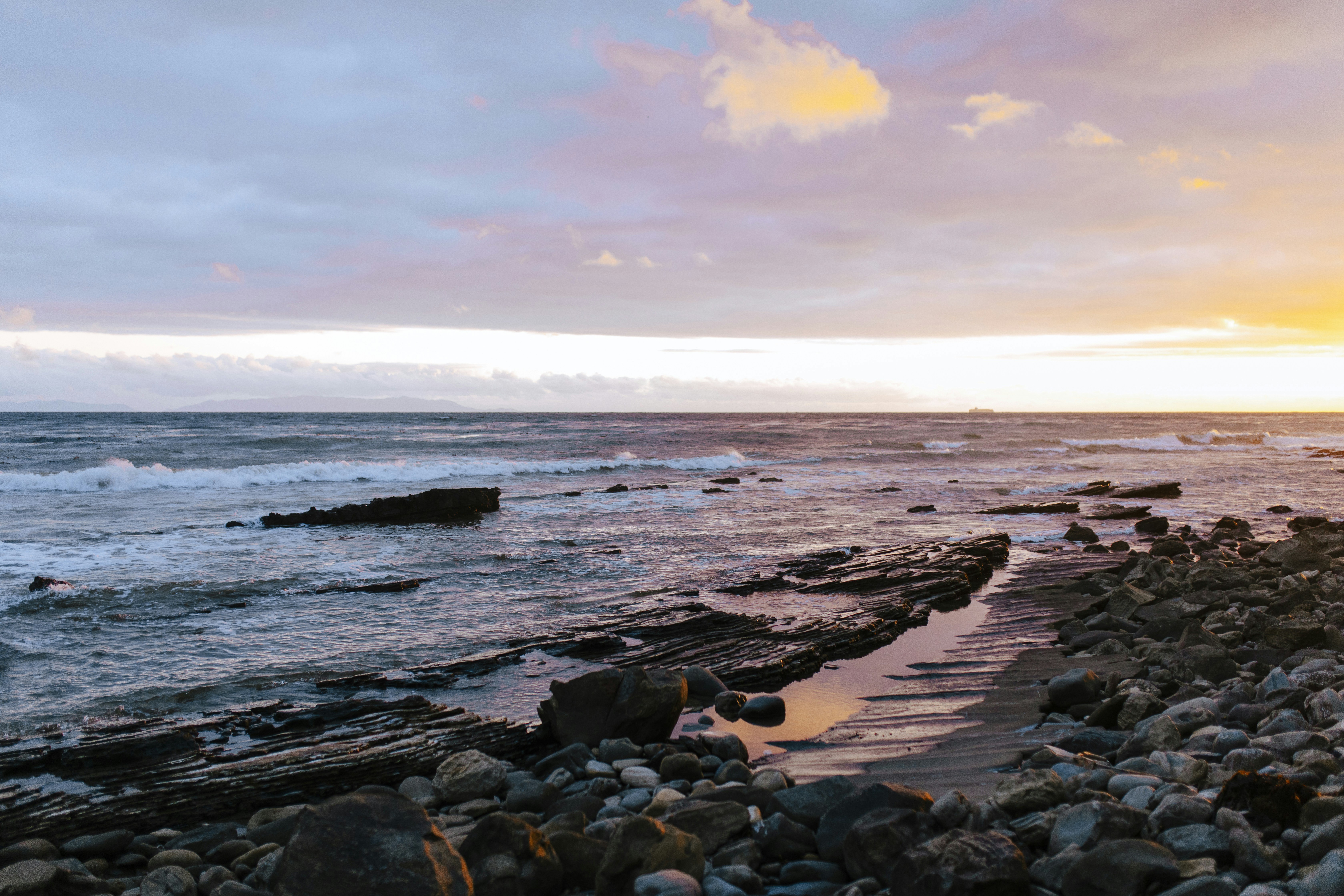 Ocean waves gently breaking over a rocky shoreline at sunset, with a vibrant sky reflecting in tidal pools.