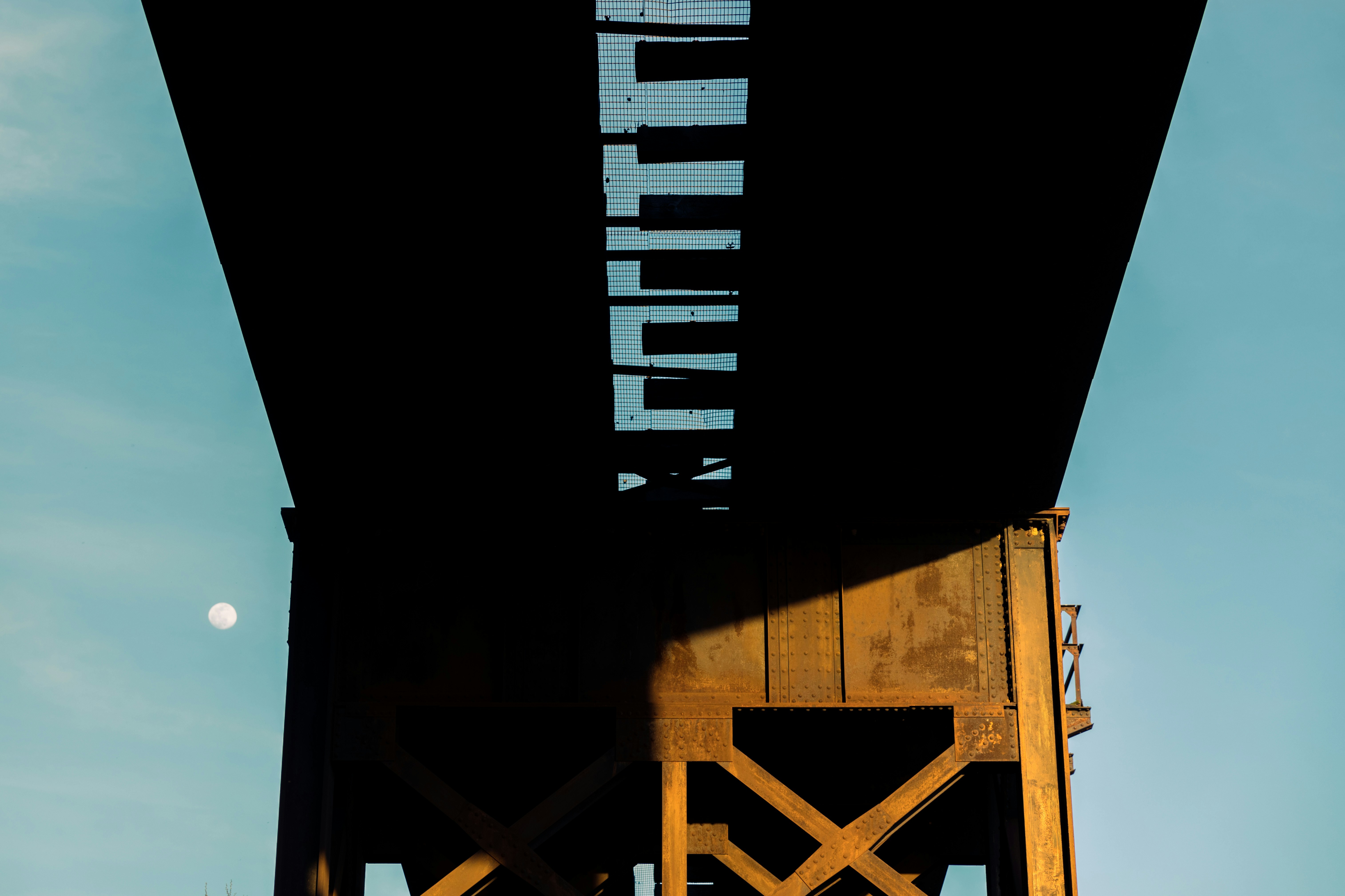 Silhouette of a wooden bridge against a blue sky with a visible moon.