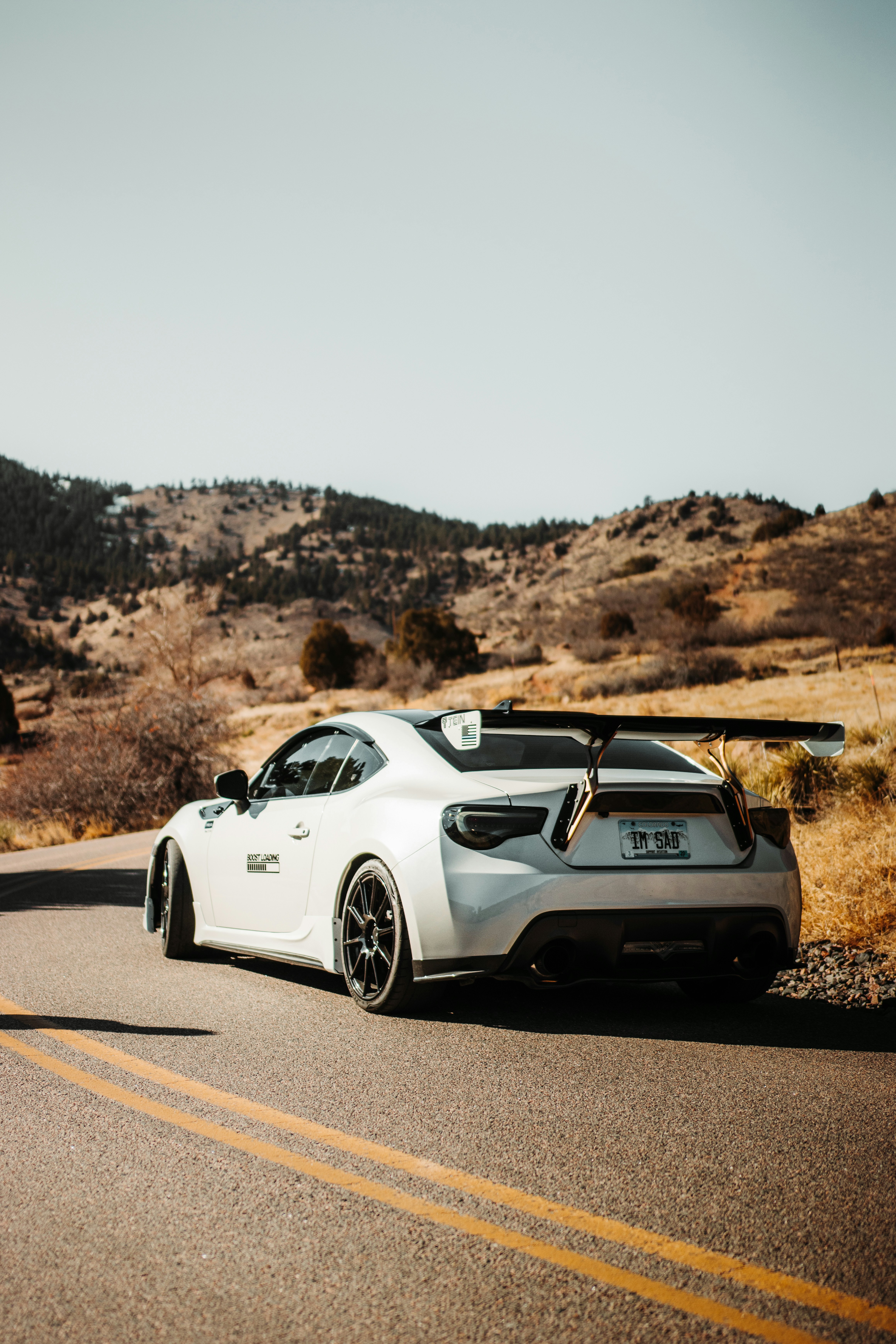 White sports coupe on a winding desert highway with a distant ridge