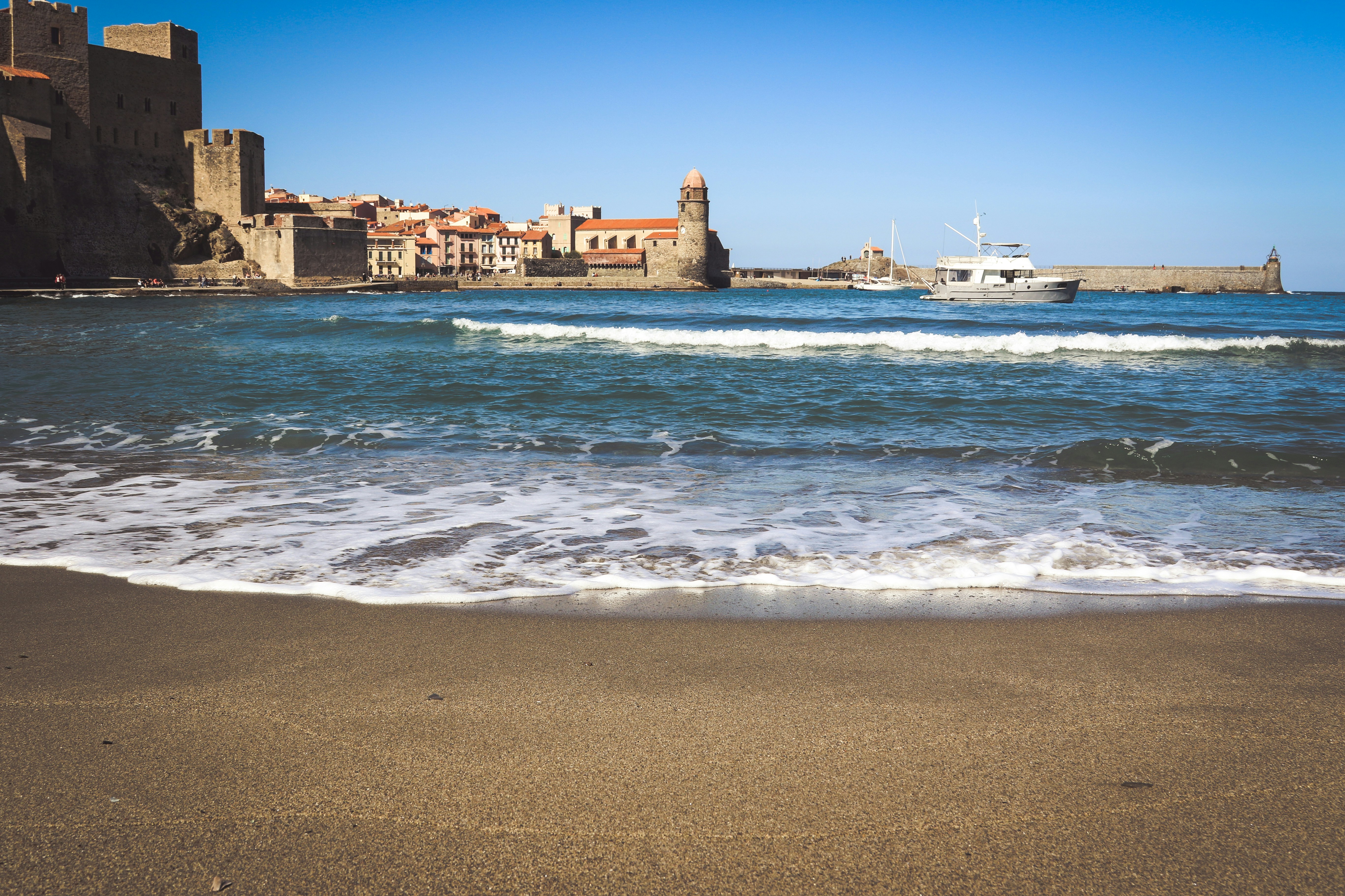 A tranquil beach scene featuring gentle waves lapping at the shore, with a picturesque harbor and historic buildings in the background.