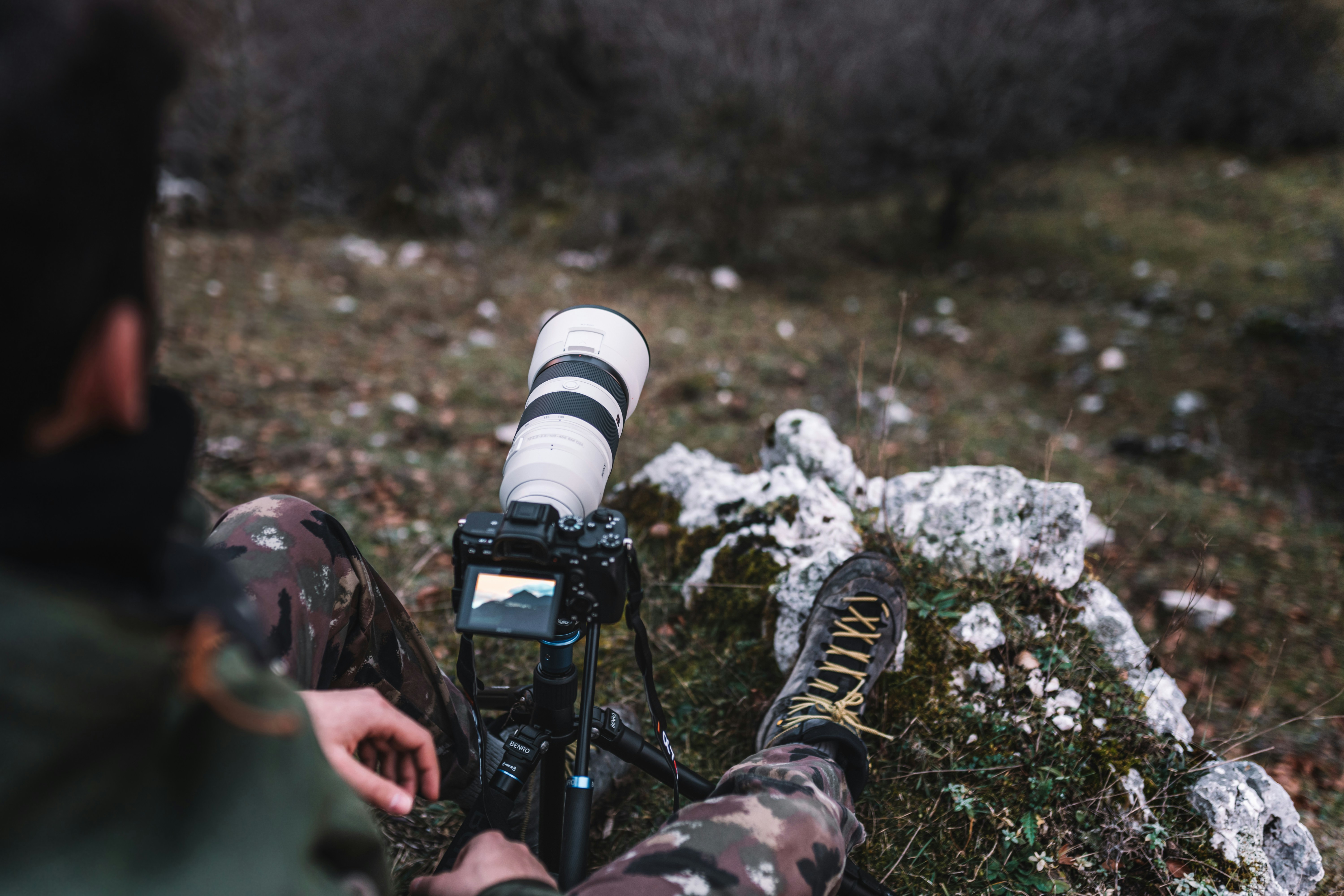Grounded Telephoto Moment: Field Photographer Ready with a White Lens in a Snow-Dusted Meadow