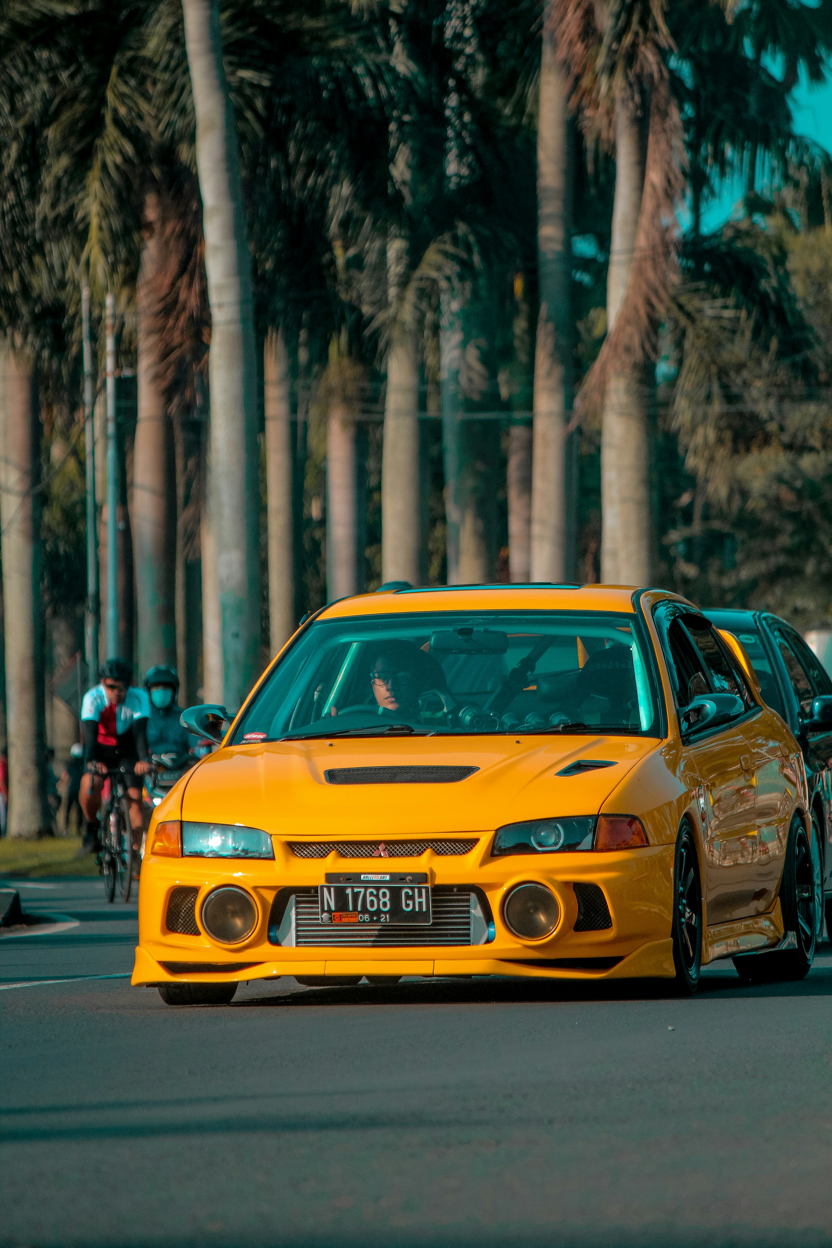 Yellow sports car was crossing a road full of palm trees 