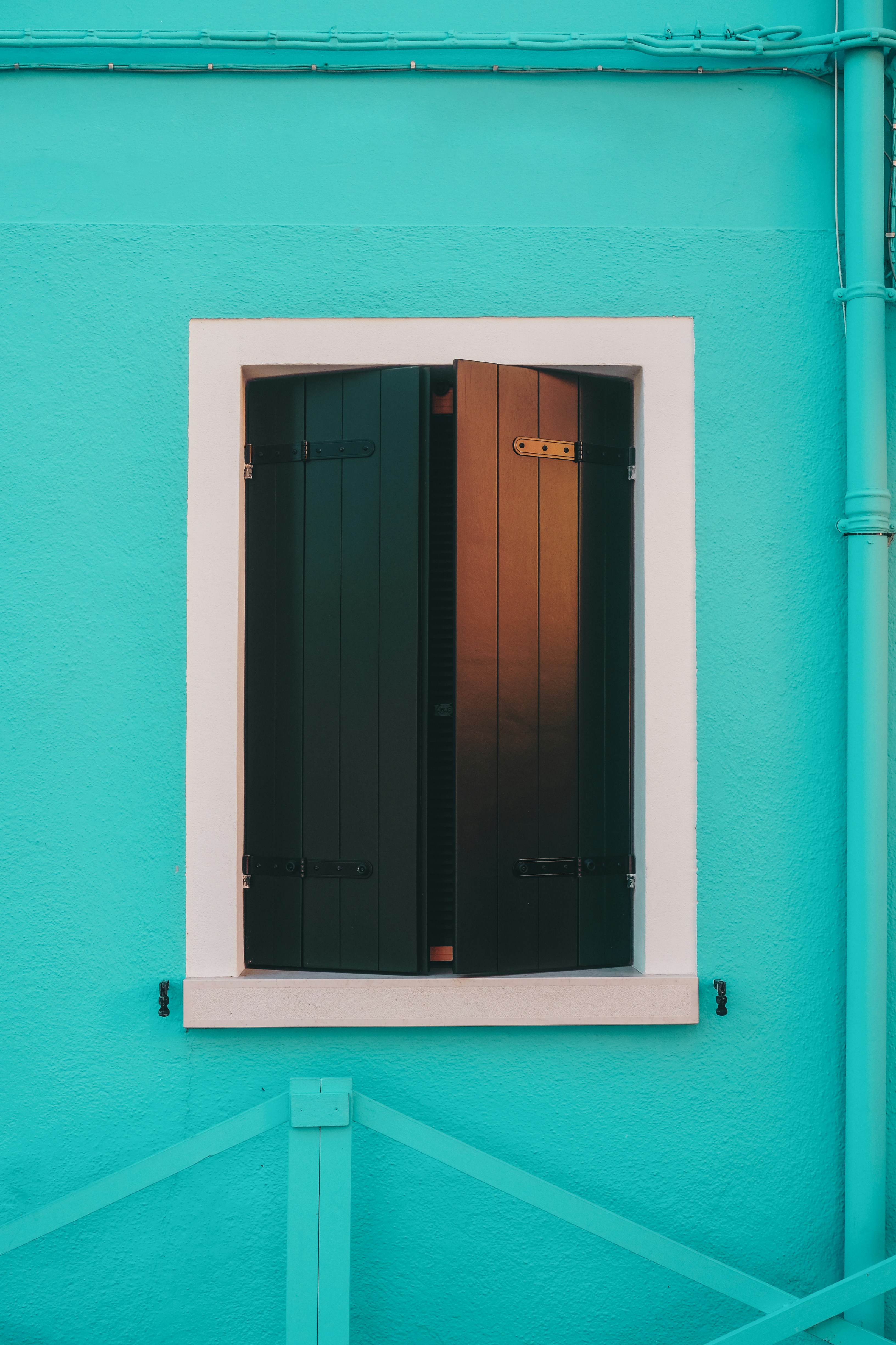 Dark wooden shutters ajar against a bright turquoise wall, revealing a glimpse of the interior. The contrast creates a striking visual appeal.