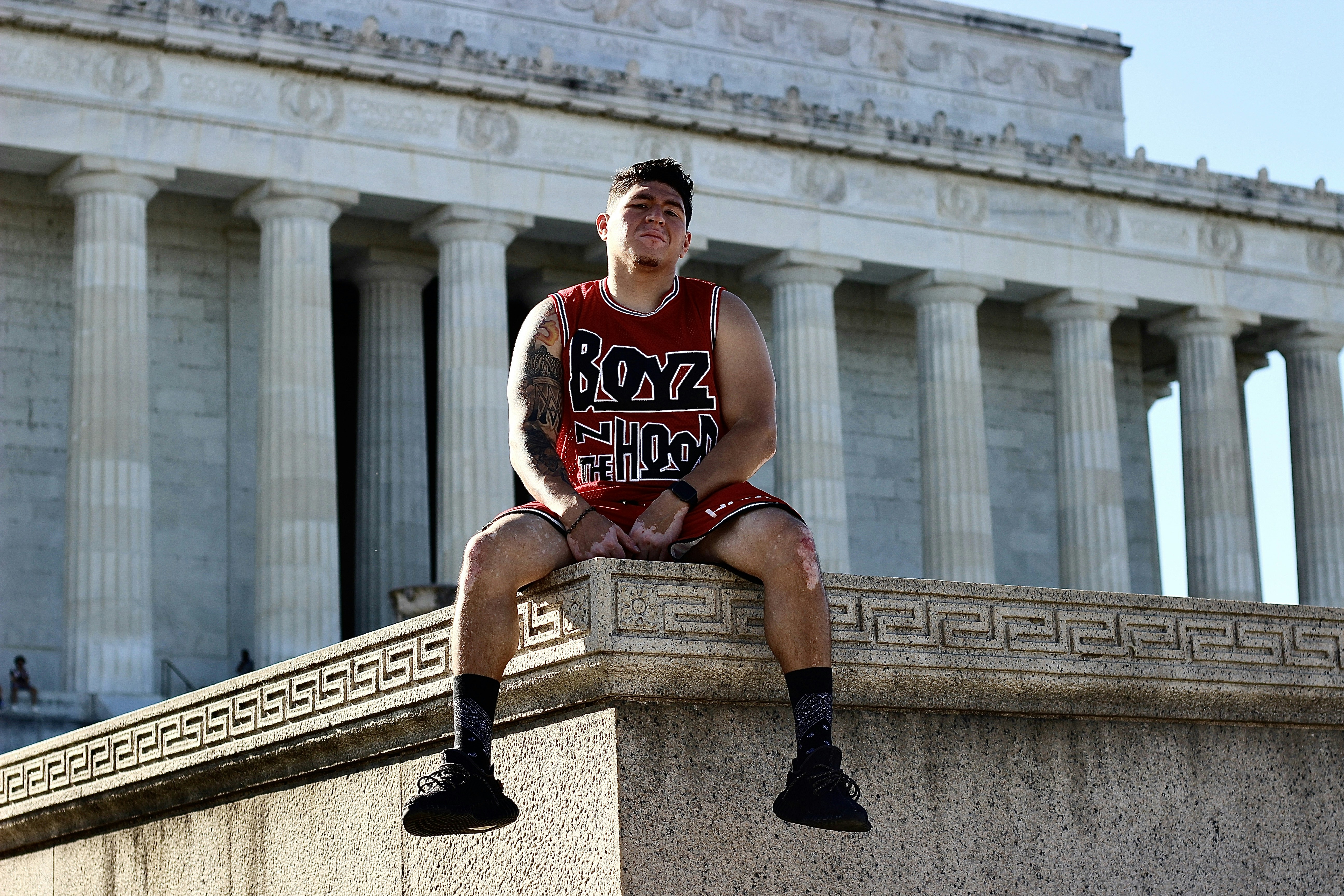 man in red and white tank top sitting on concrete bench during daytime