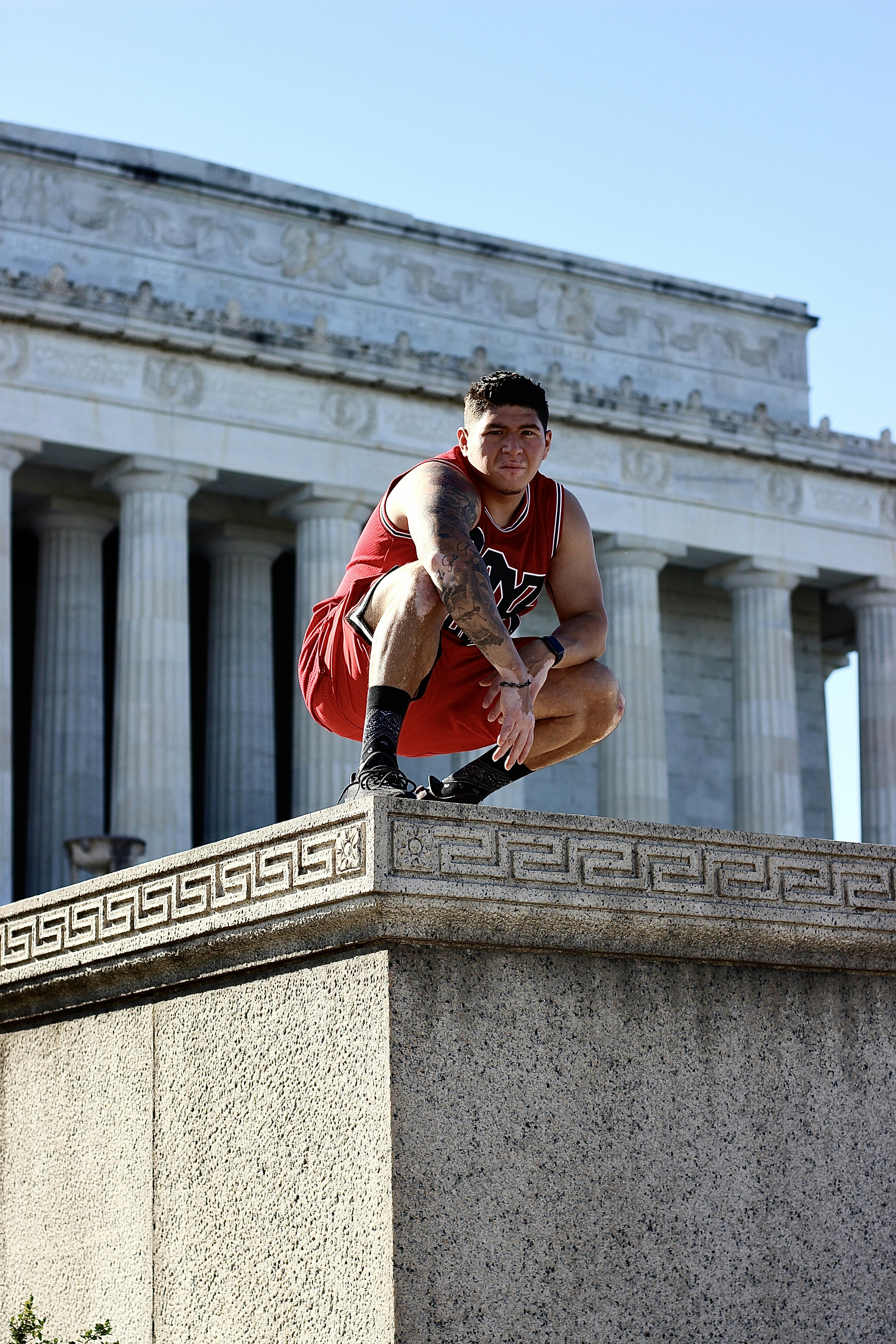 man in red t-shirt and black pants sitting on concrete bench during daytime