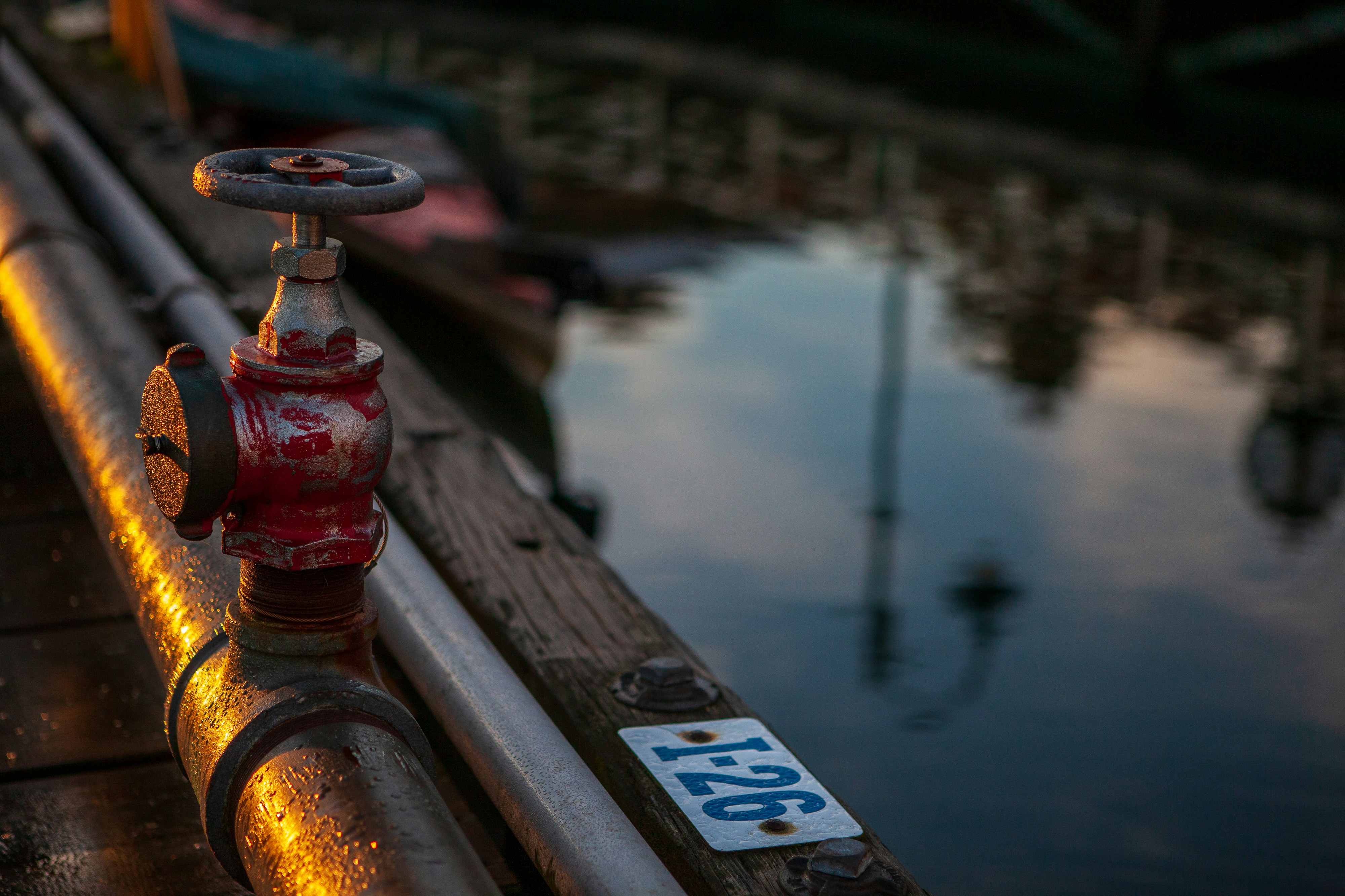 Close-up of a weathered valve on a wooden dock, reflecting the evening light on calm water.