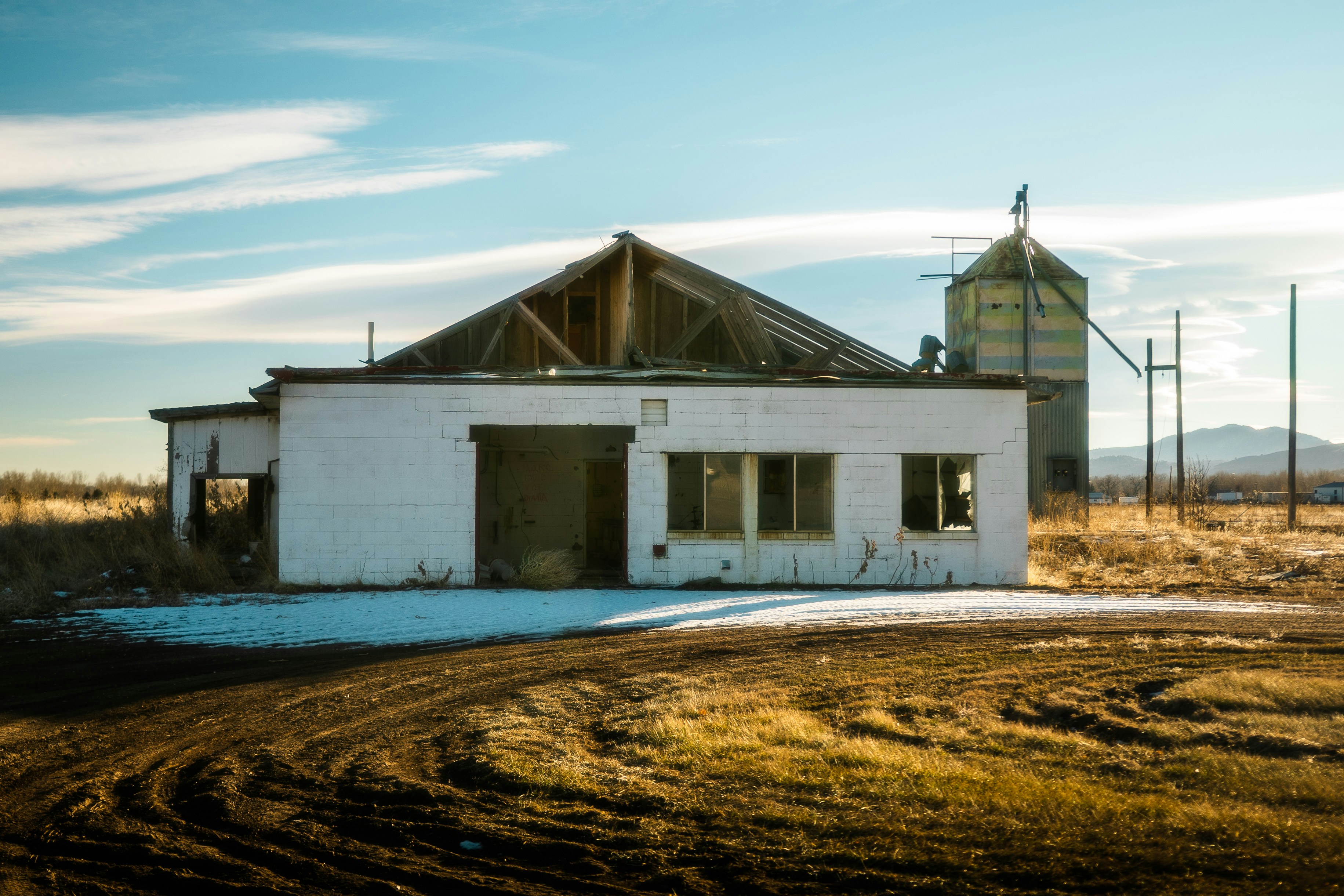 Weathered white building with a sloped roof stands near a calm water body, under a clear blue sky.