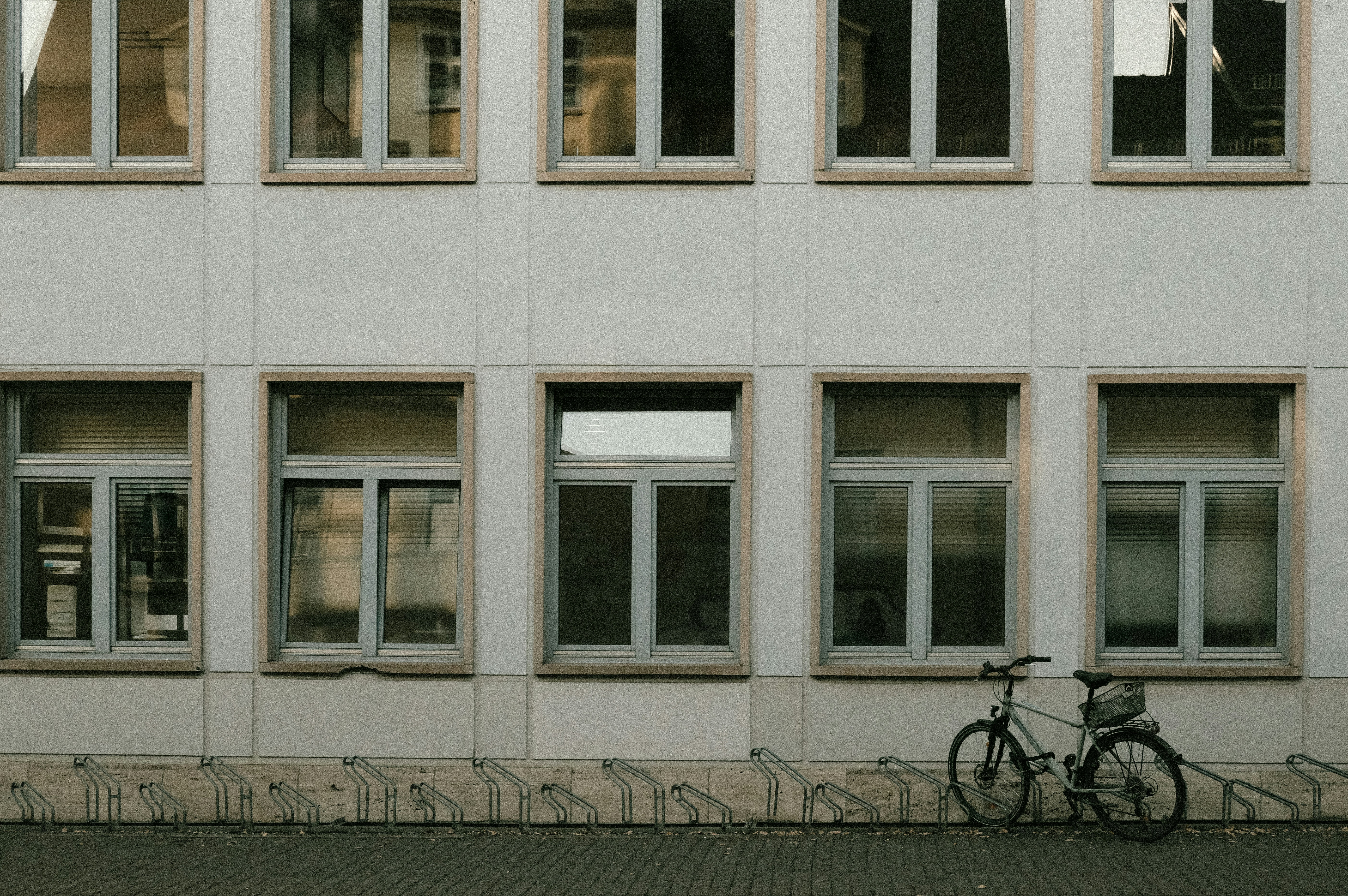 A bicycle rests against a minimalist building facade, framed by large windows that reflect the urban environment.