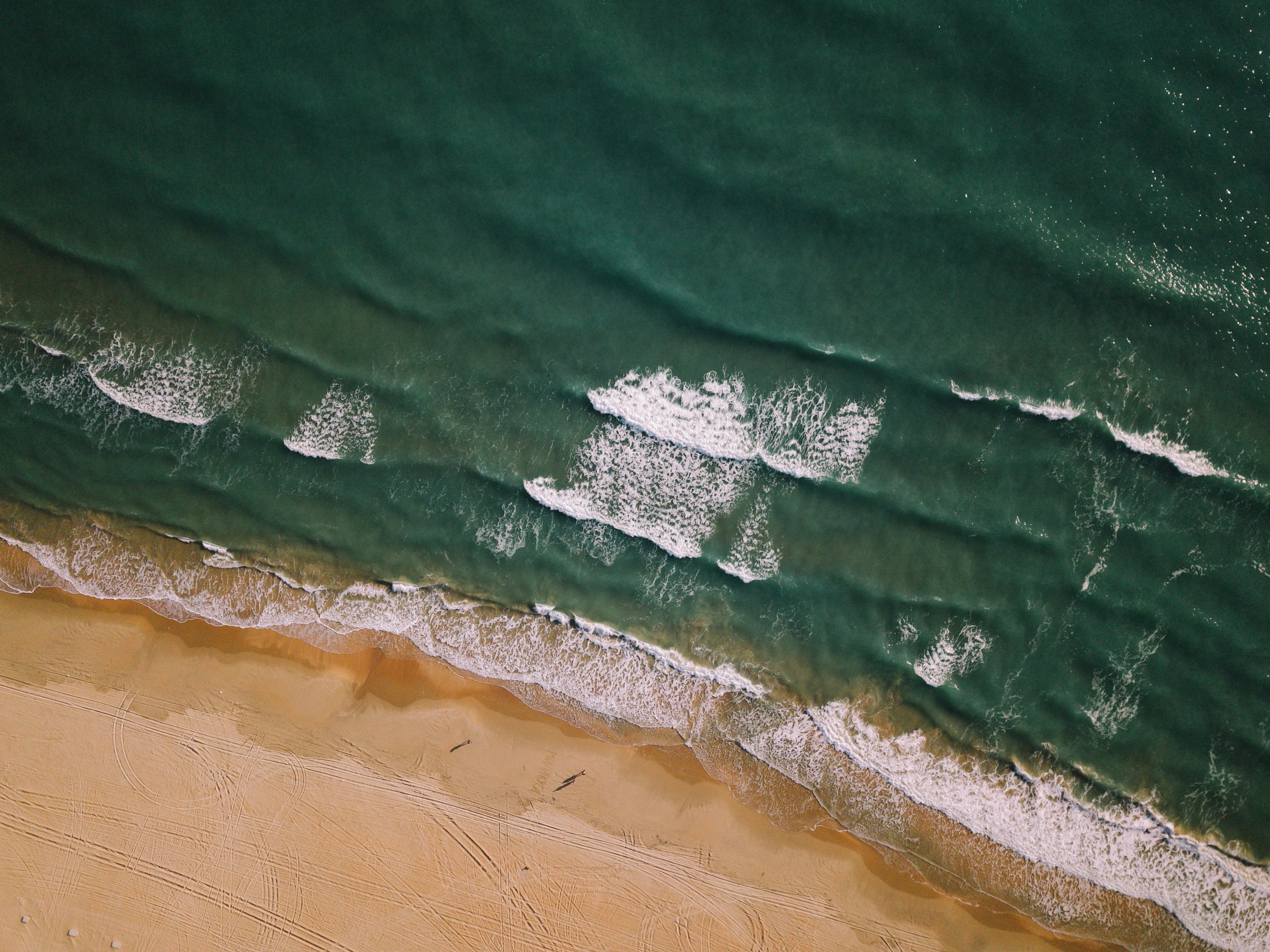 Aerial view of waves gently crashing onto a sandy beach, forming parallel lines of white foam.