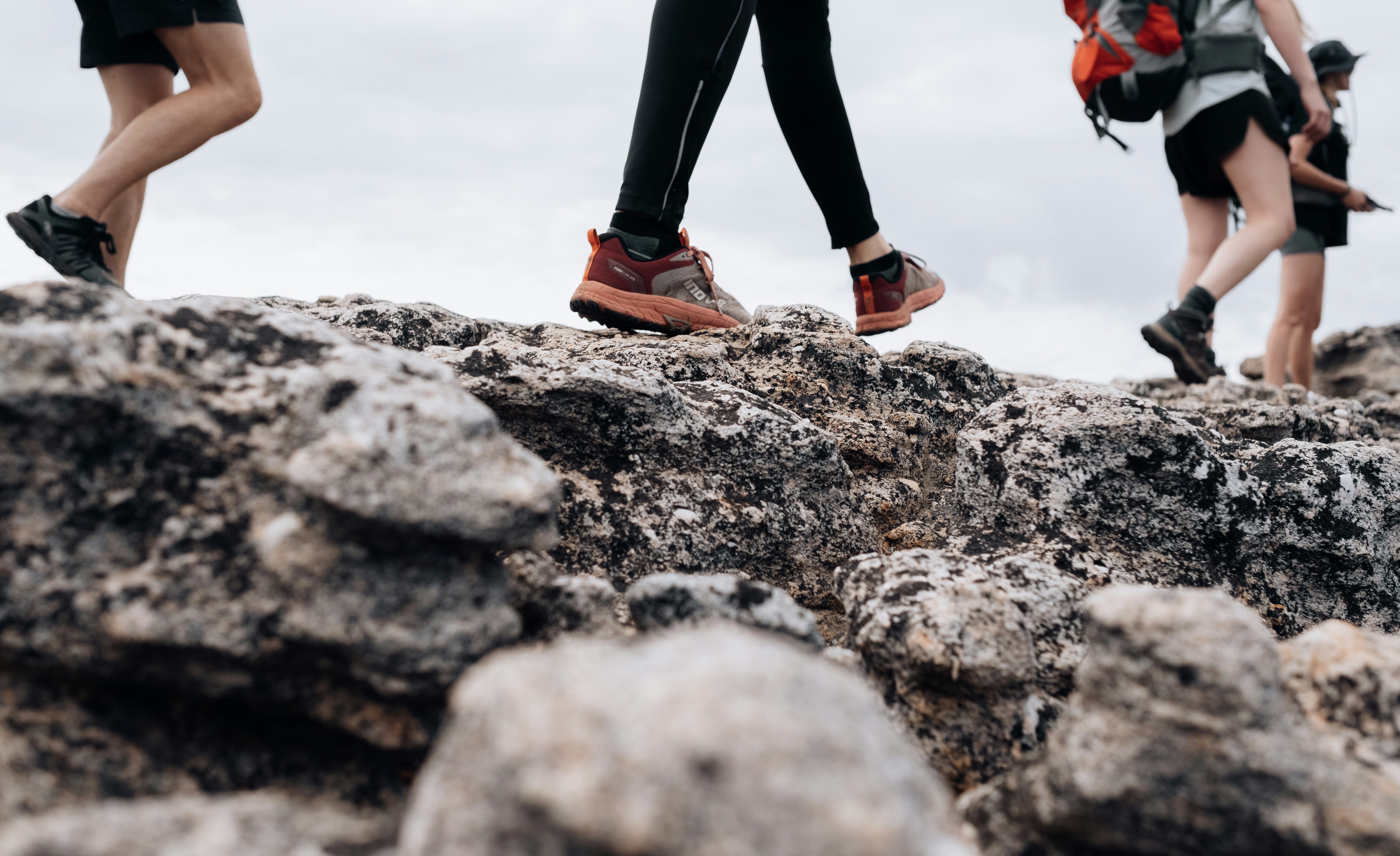 Hikers navigating rugged rocks on a trail, showcasing their footwear and determination. The scene captures the essence of adventure and exploration.