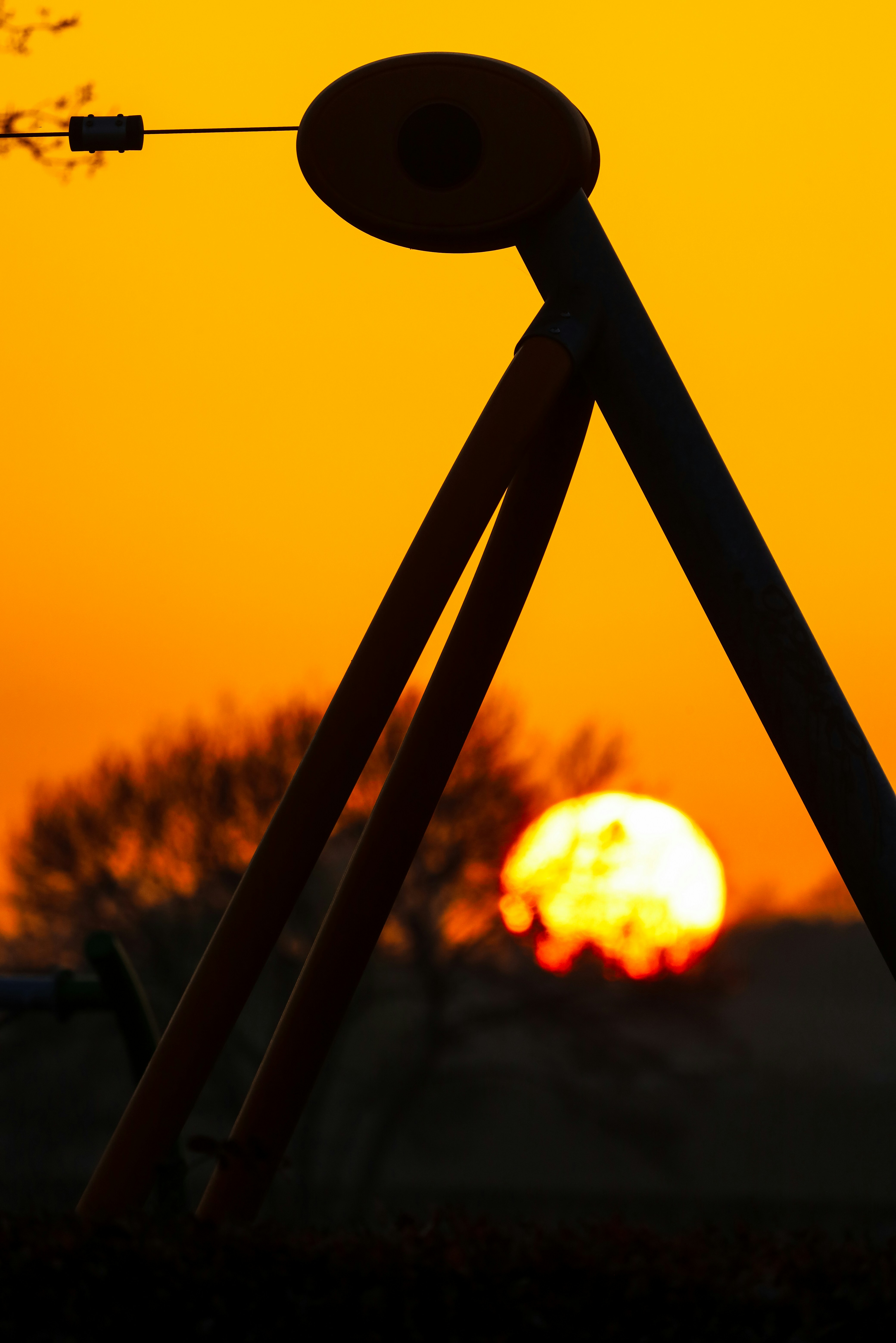A silhouetted surveying instrument stands prominently against a vibrant sunset, with the sun's glowing orb partially visible in the background.