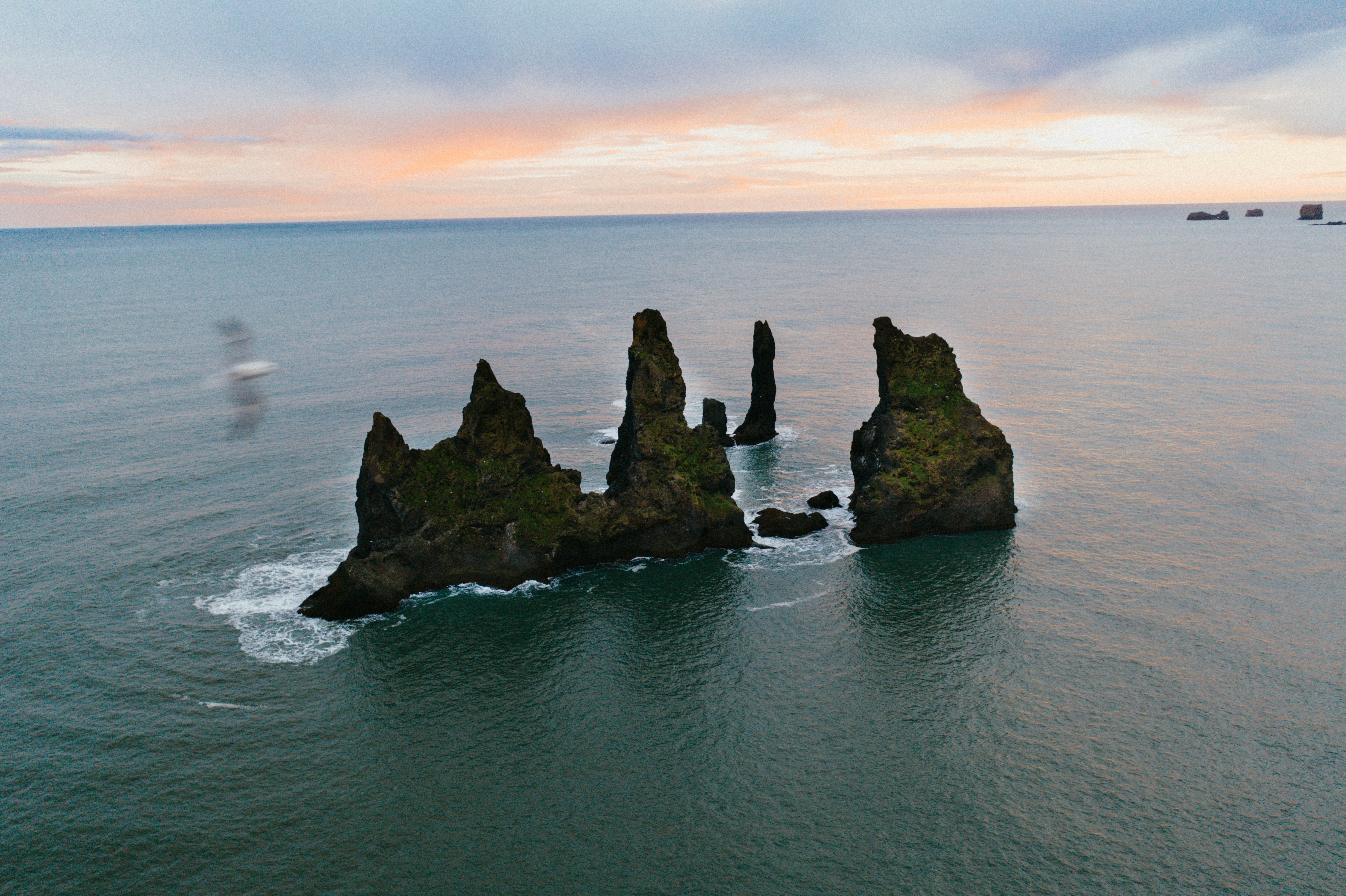 Majestic rock spires rise from the ocean under a pastel sky, with gentle waves lapping at their bases.
