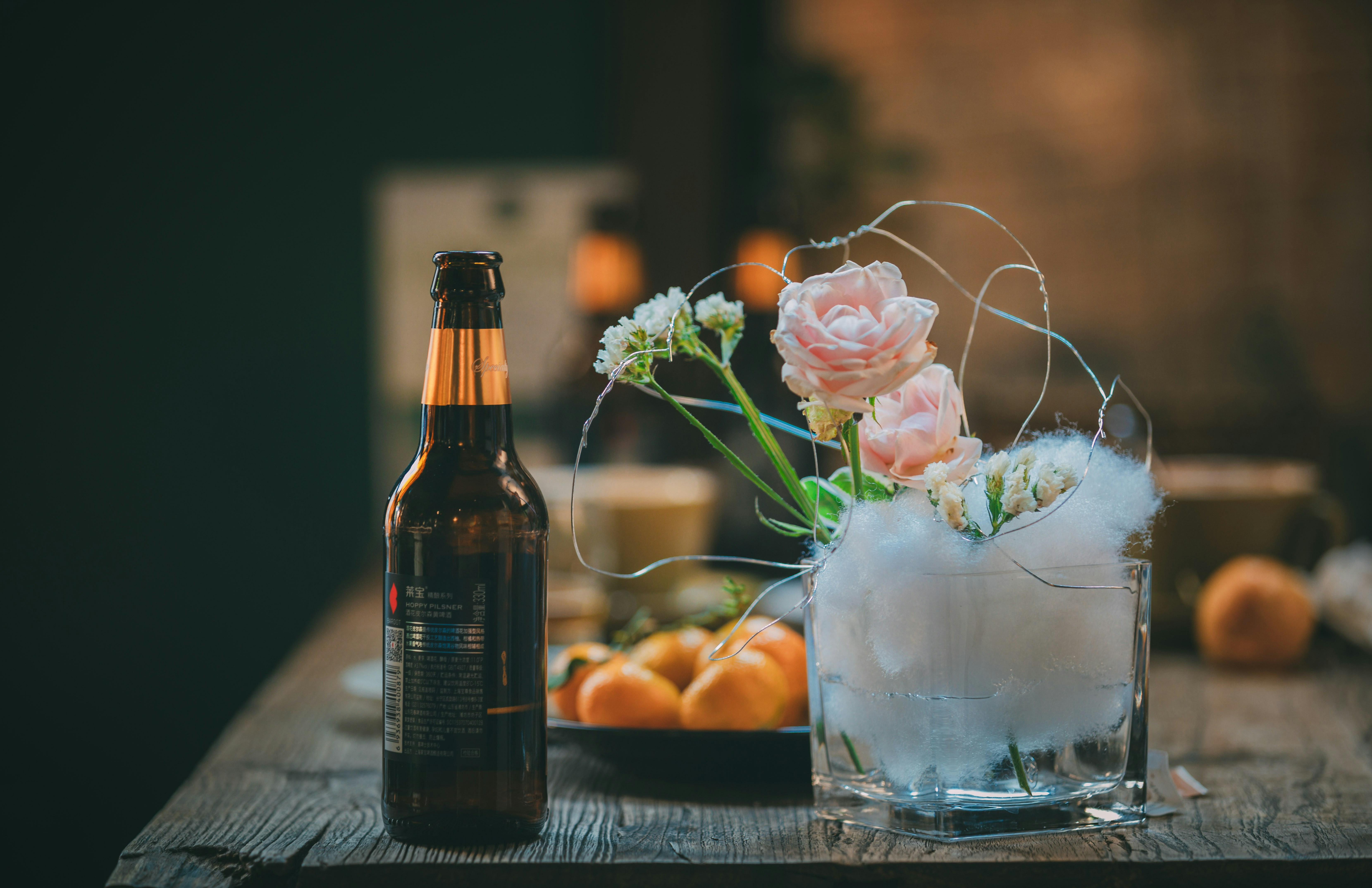 Bottle on the Rustic Table: A Quiet Still Life with a Glass Vase and Pink Petals