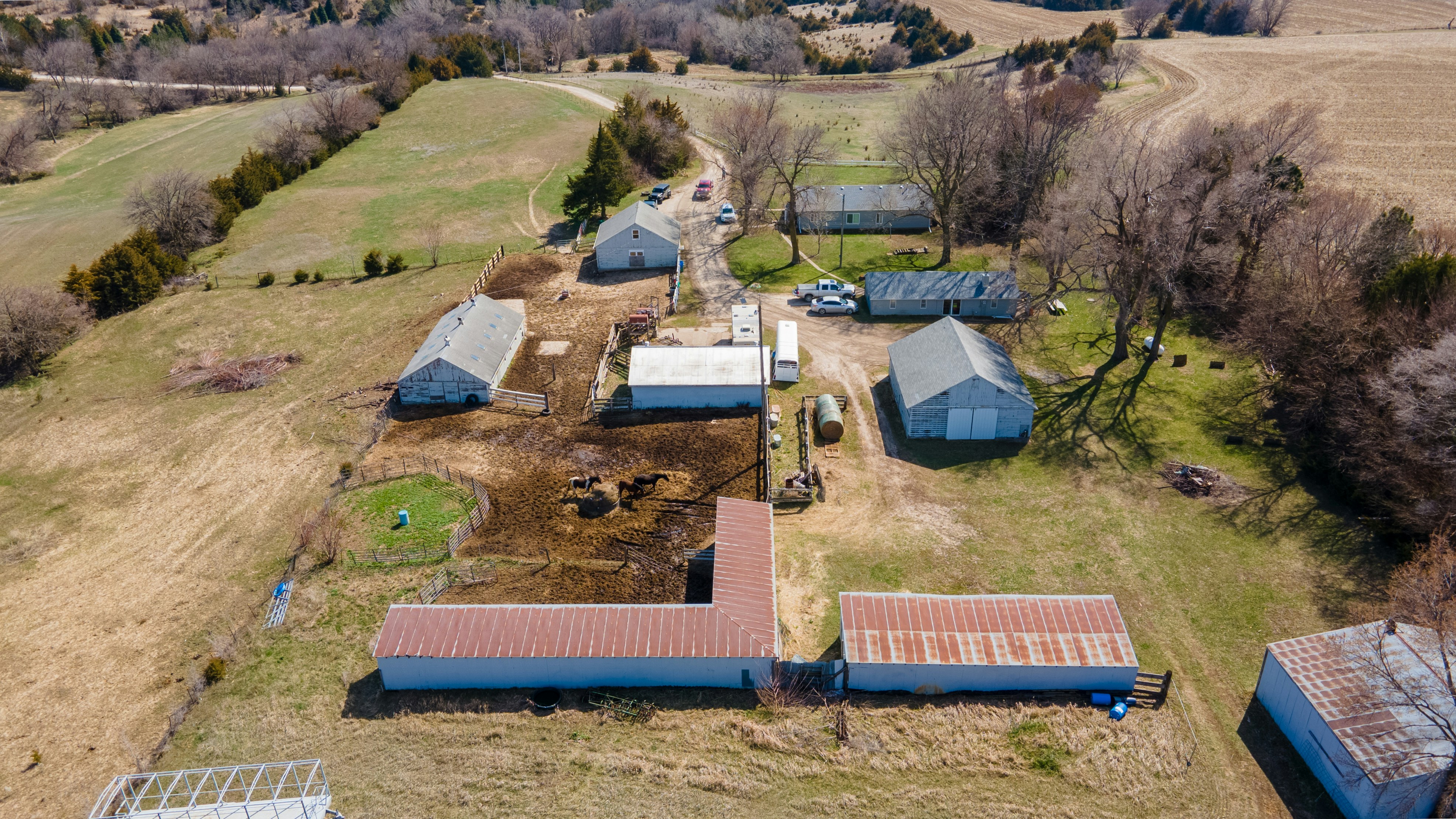 Aerial view of a farm layout with multiple buildings and open fields surrounded by trees.