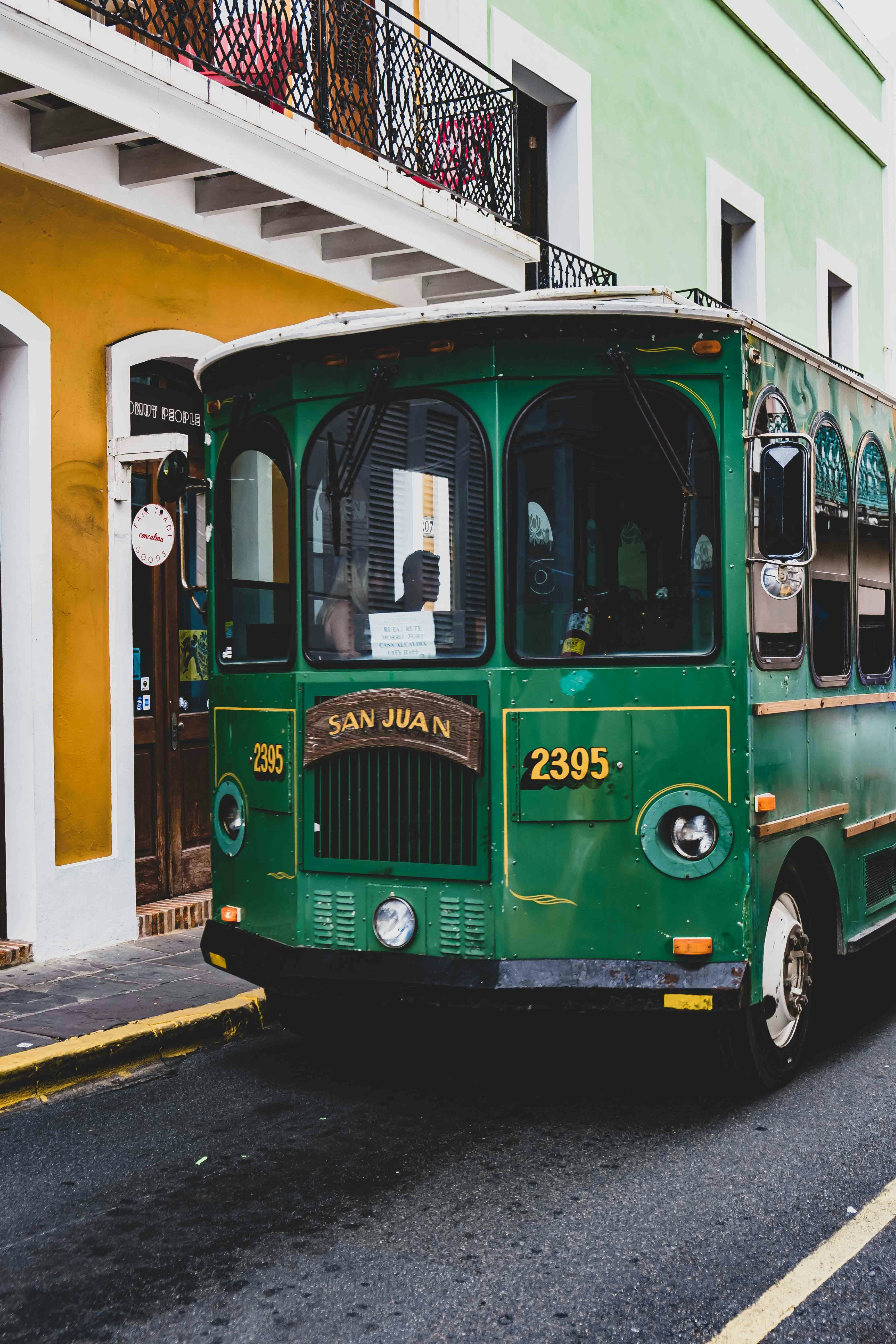 Green trolley bus parked on a colorful street in San Juan, showcasing the vibrant architecture and local charm.