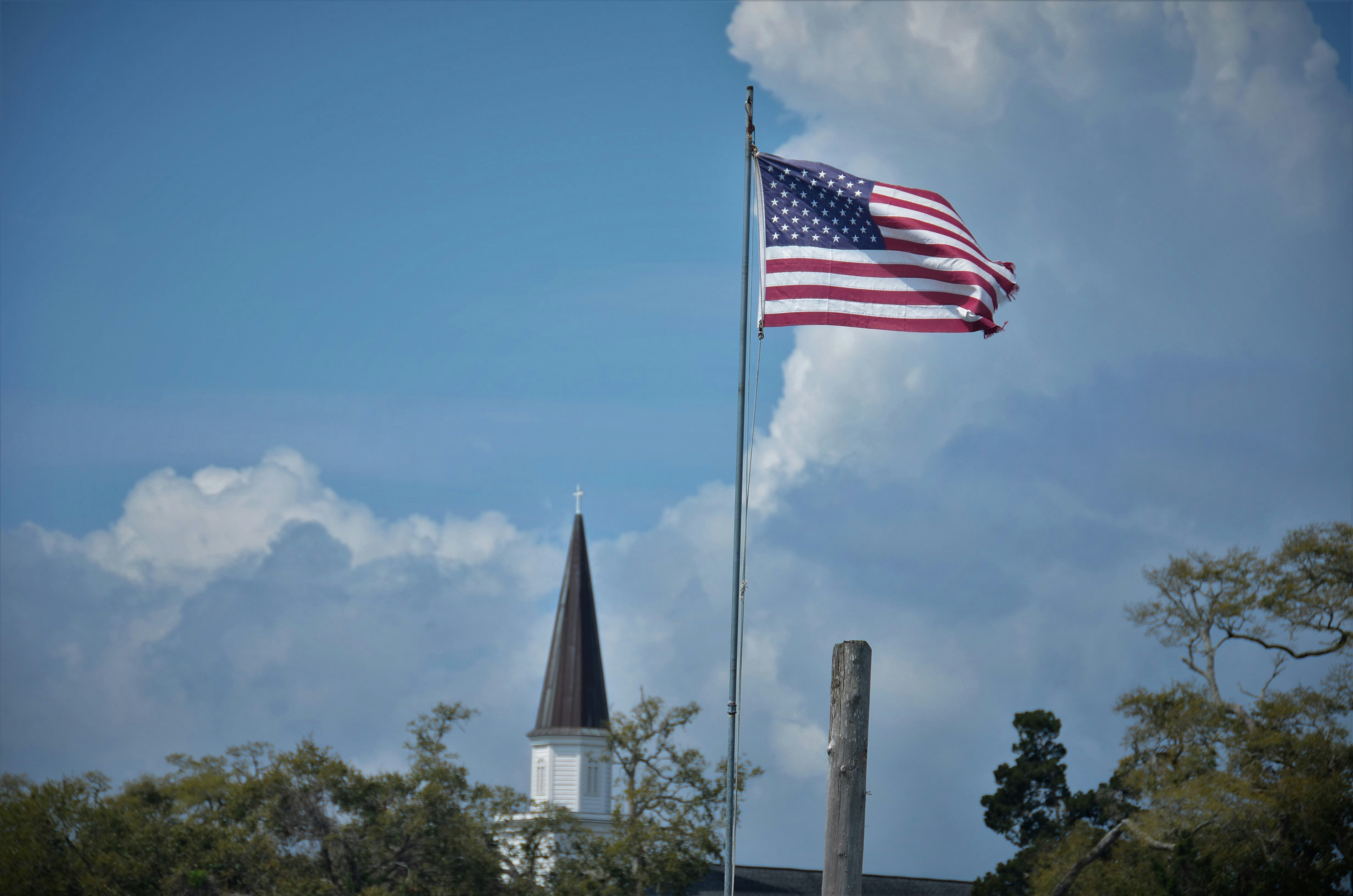 Wind-Tugged Flag Above a White Church Steeple in a Quiet Town