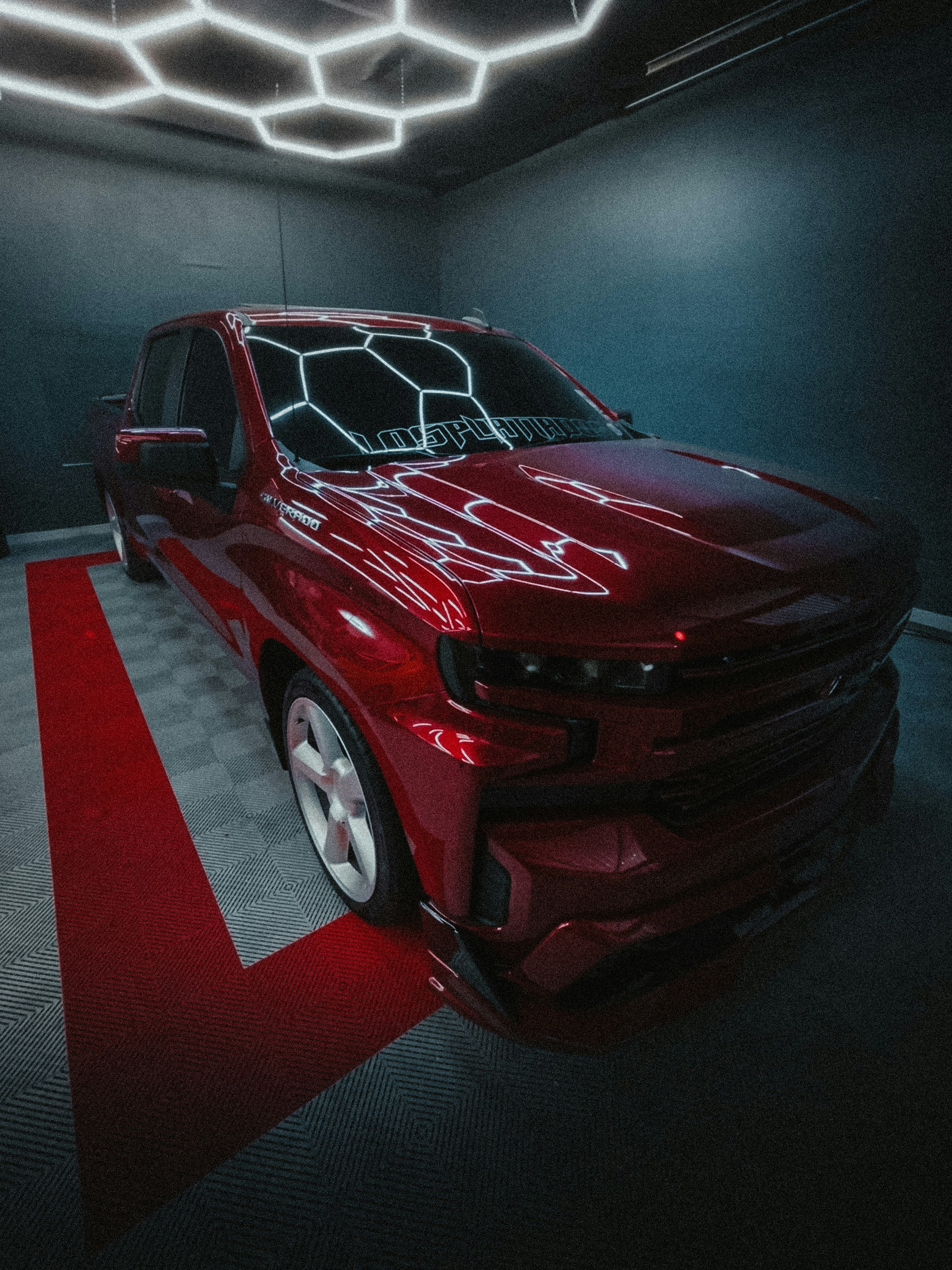 A striking red pickup truck showcased in a dimly lit garage, illuminated by geometric neon lights and a bold red arrow on the floor.