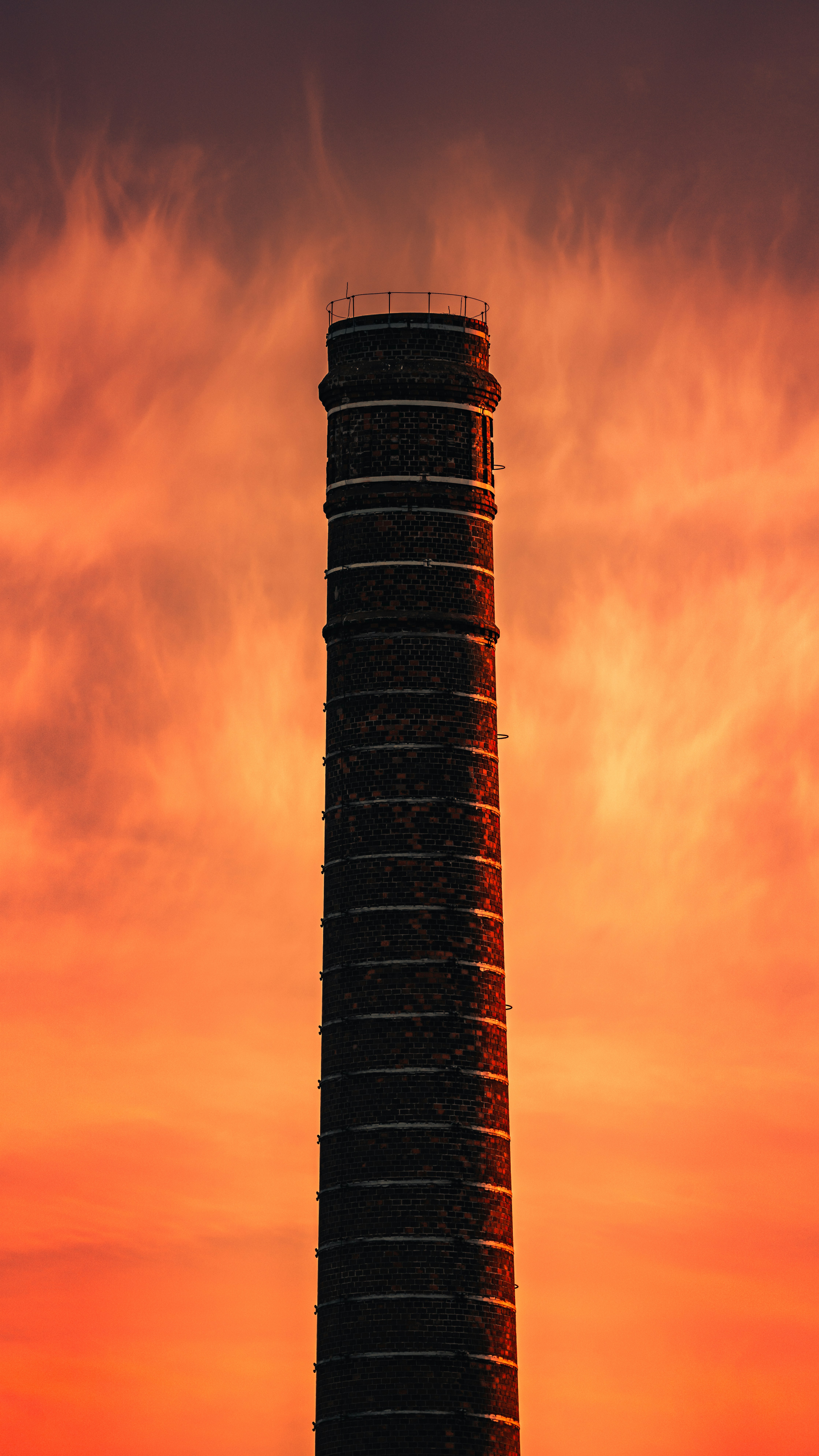 Tall chimney silhouetted against a fiery sky resembling flames.