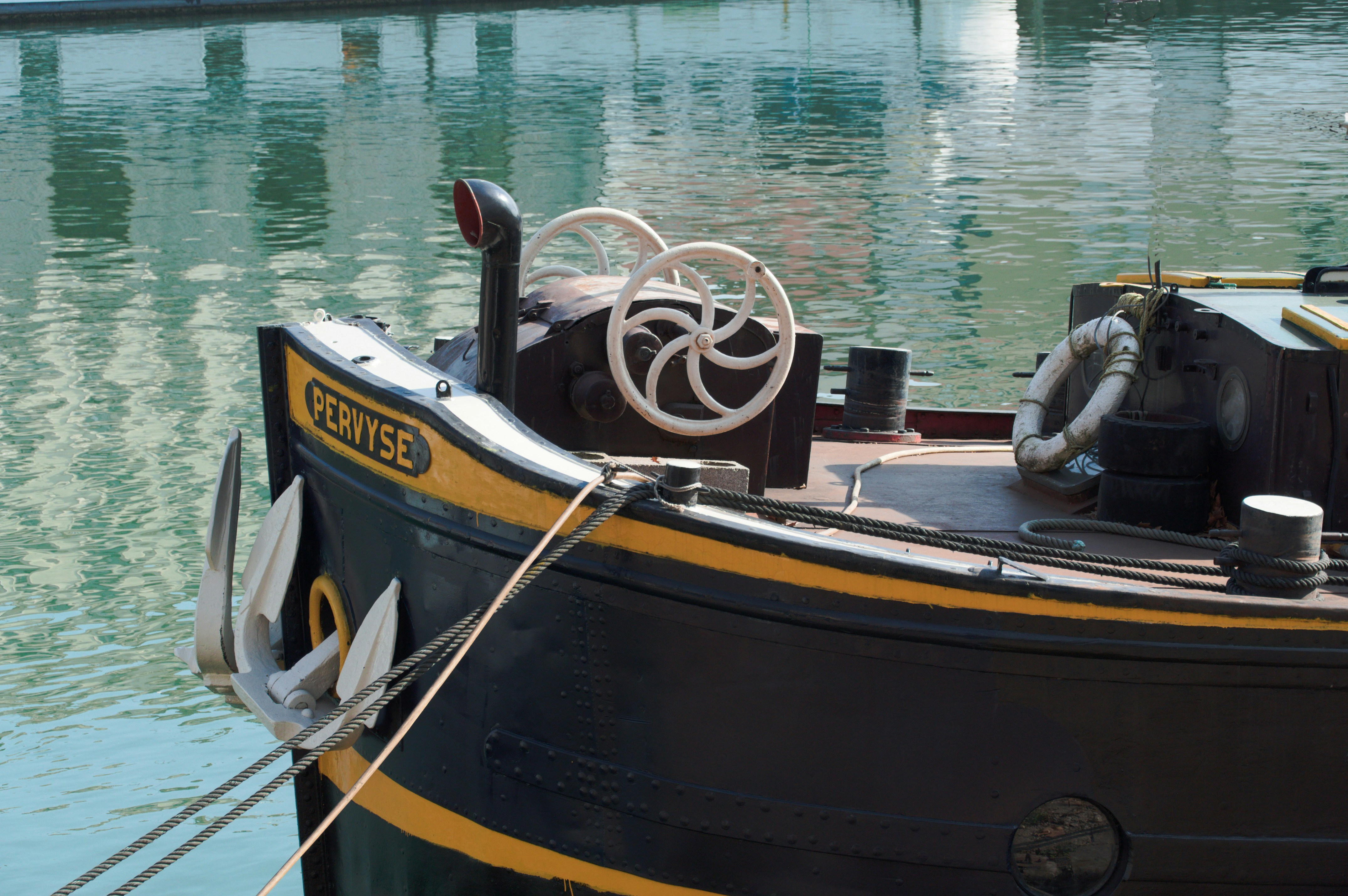 Bow of a classic boat with intricate white steering wheel, moored on calm reflective waters.