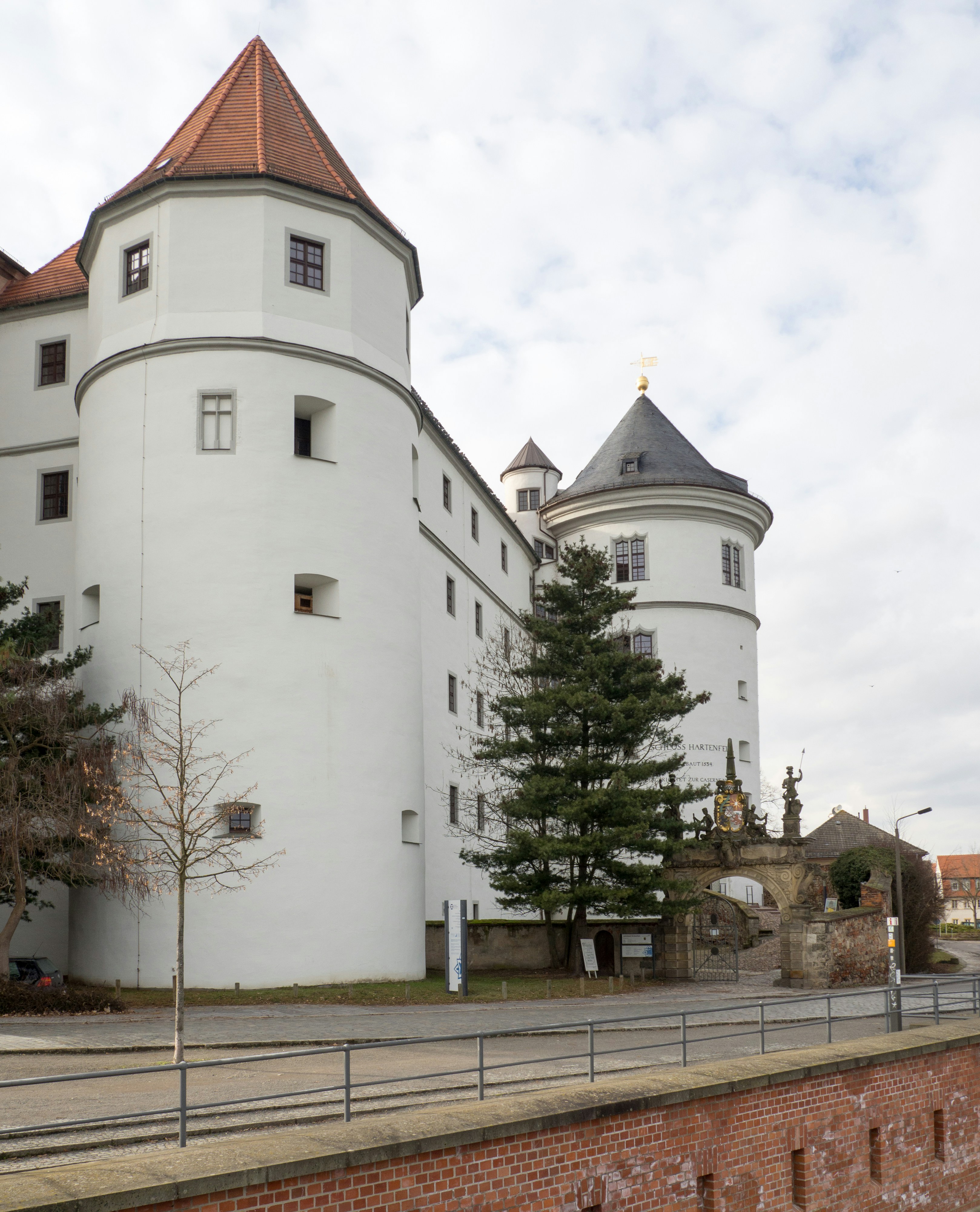Historic castle structure featuring distinct round towers and a vibrant roof. Surrounded by greenery and a cobblestone path.