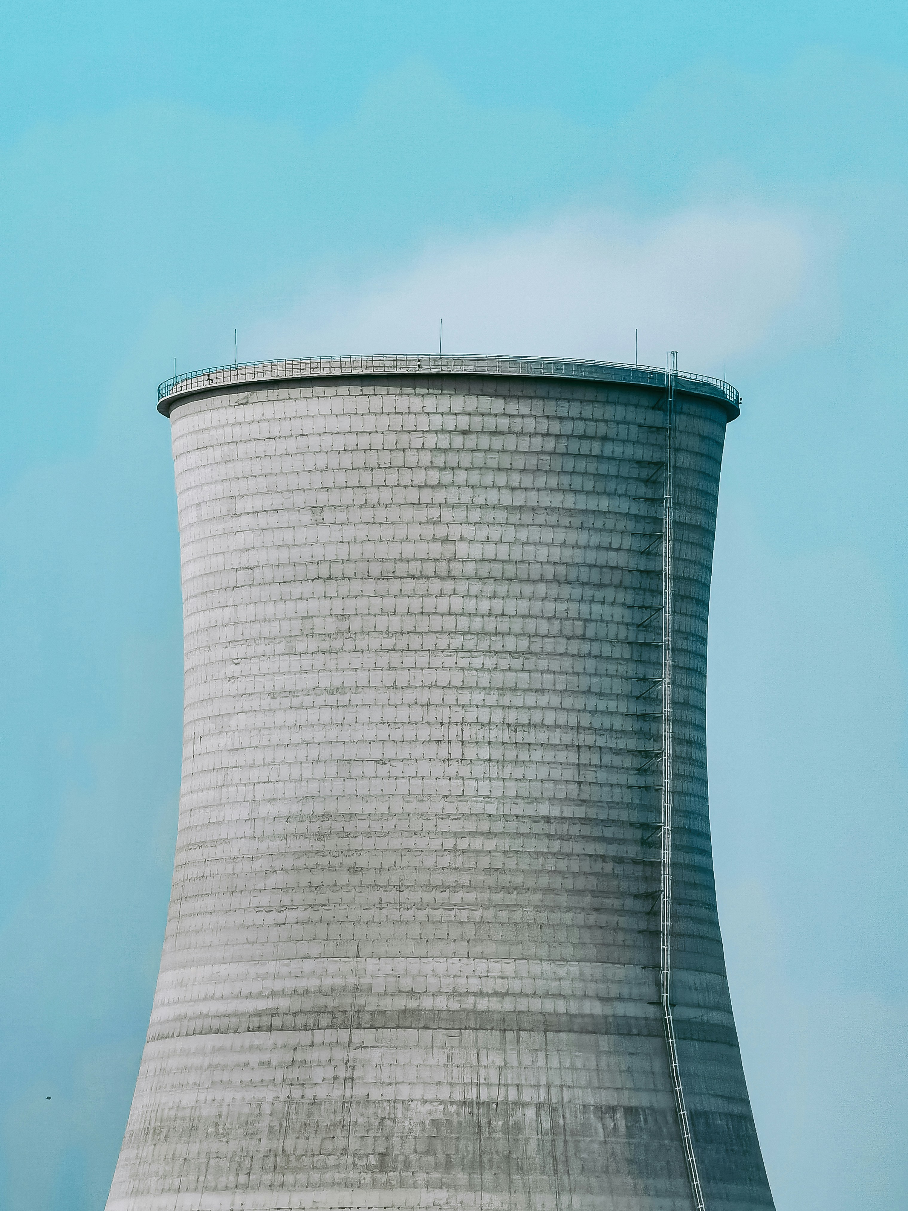 Cooling tower of a power plant rises against a clear blue sky, showcasing industrial architecture. The image highlights the tower's textured surface and minimalist design.