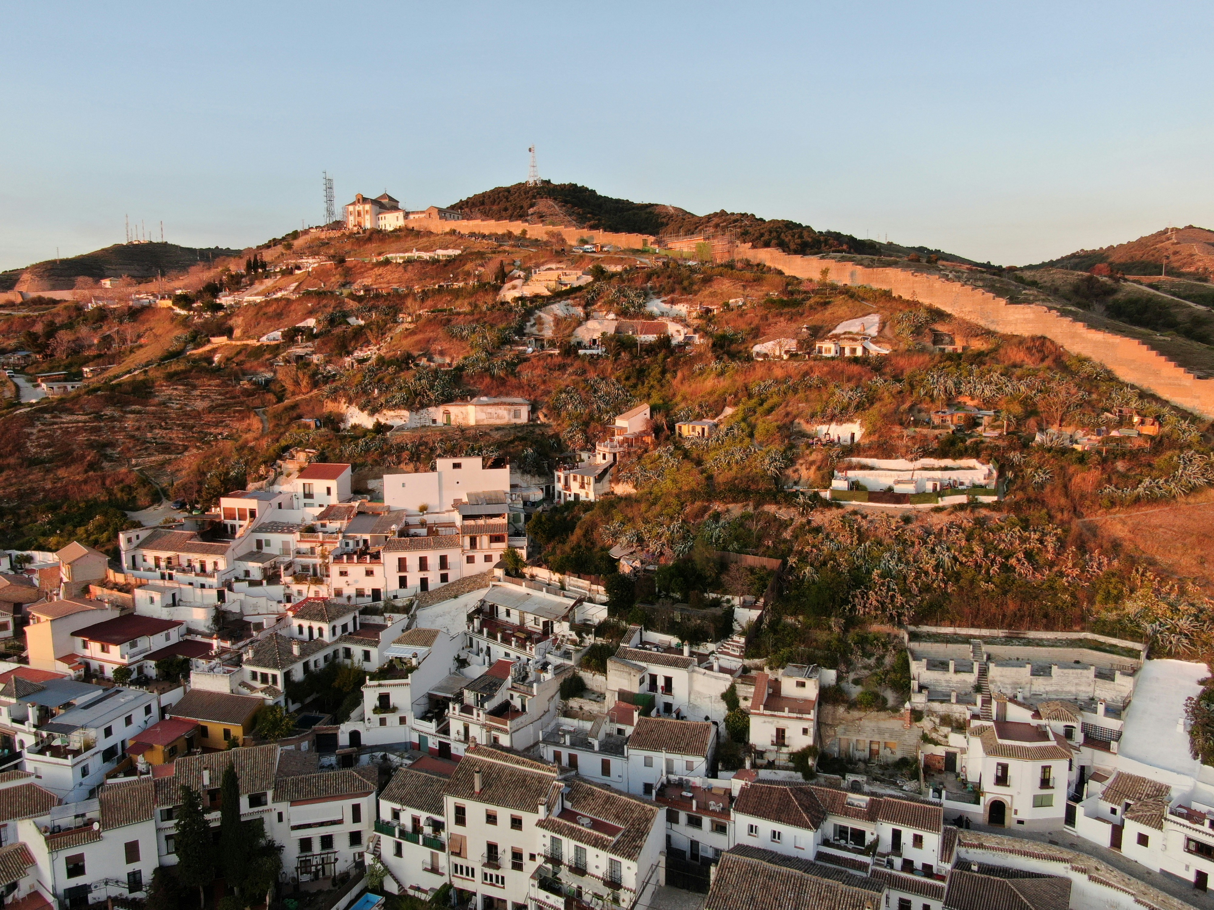 Whitewashed village nestled against a sunlit hillside under a clear sky.