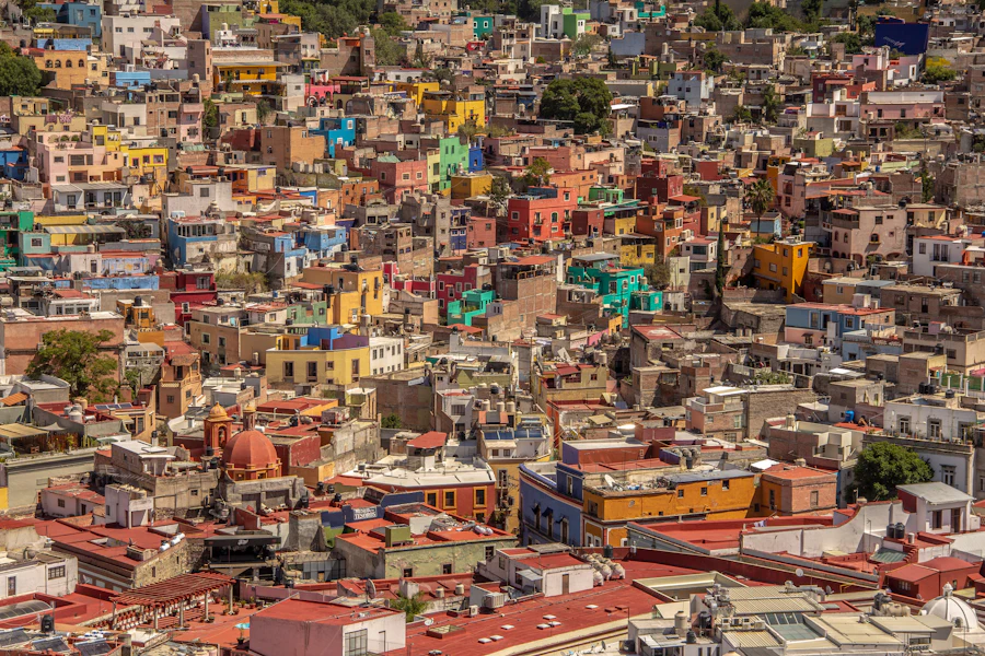 Dense hillside neighborhood packed with flat-roofed buildings painted in bright blues, reds, yellows, and greens. A domed rooftop stands out amid the layered urban sprawl.