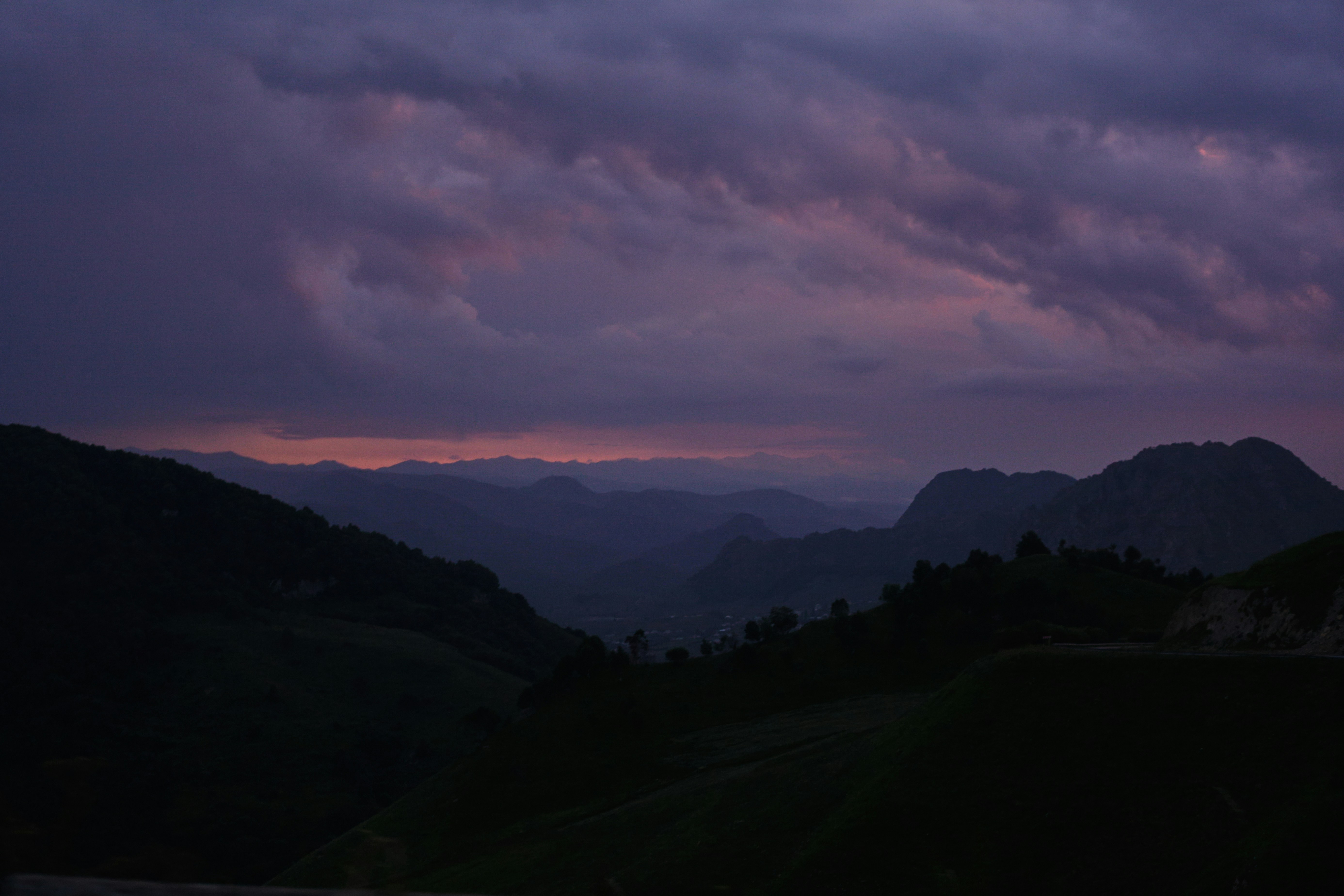 Dramatic twilight sky casts purple hues over a mountainous landscape, with layers of hills fading into the distance.