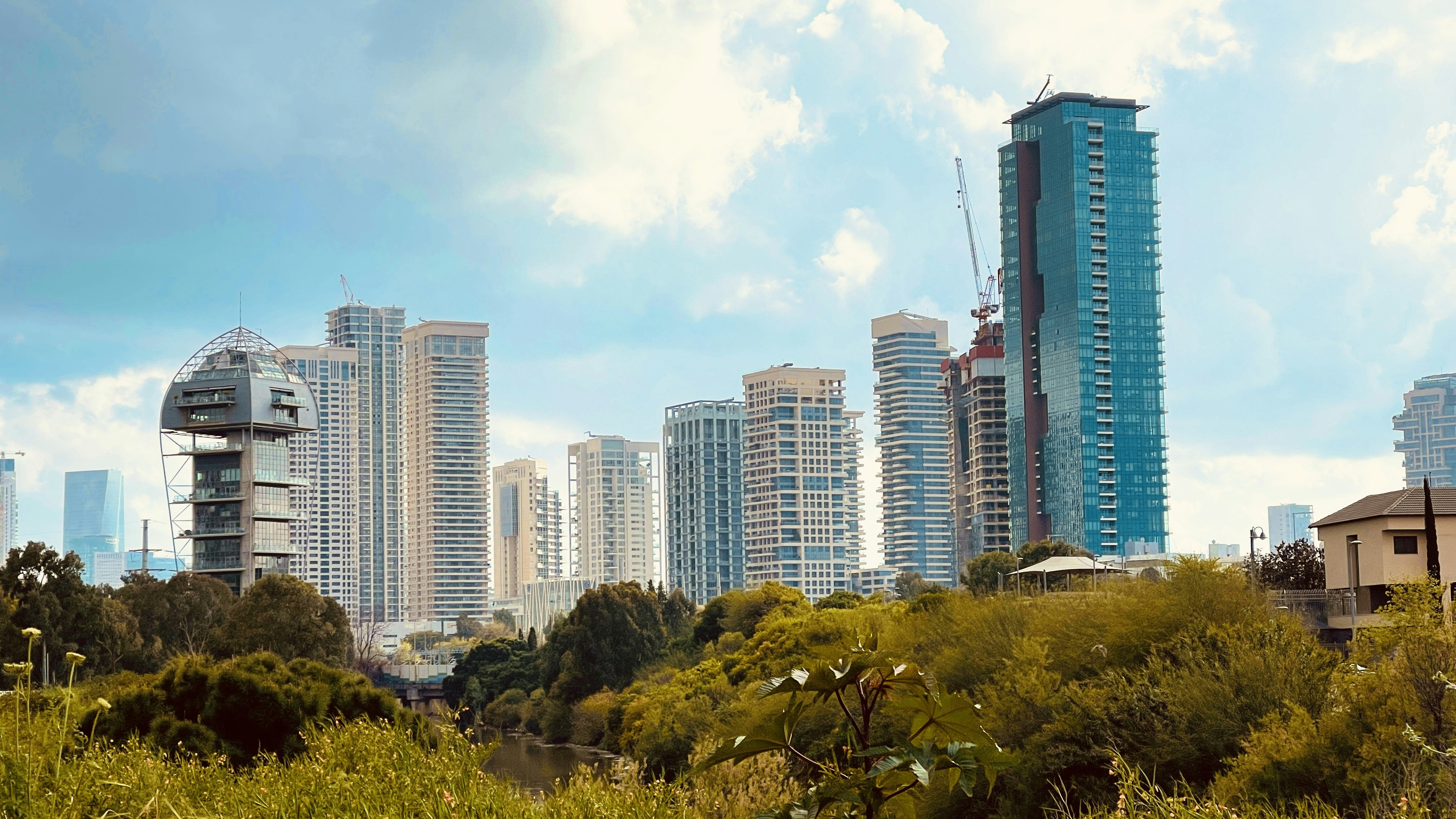 Modern skyscrapers rise above lush greenery, showcasing the blend of nature and architecture in an evolving urban landscape.