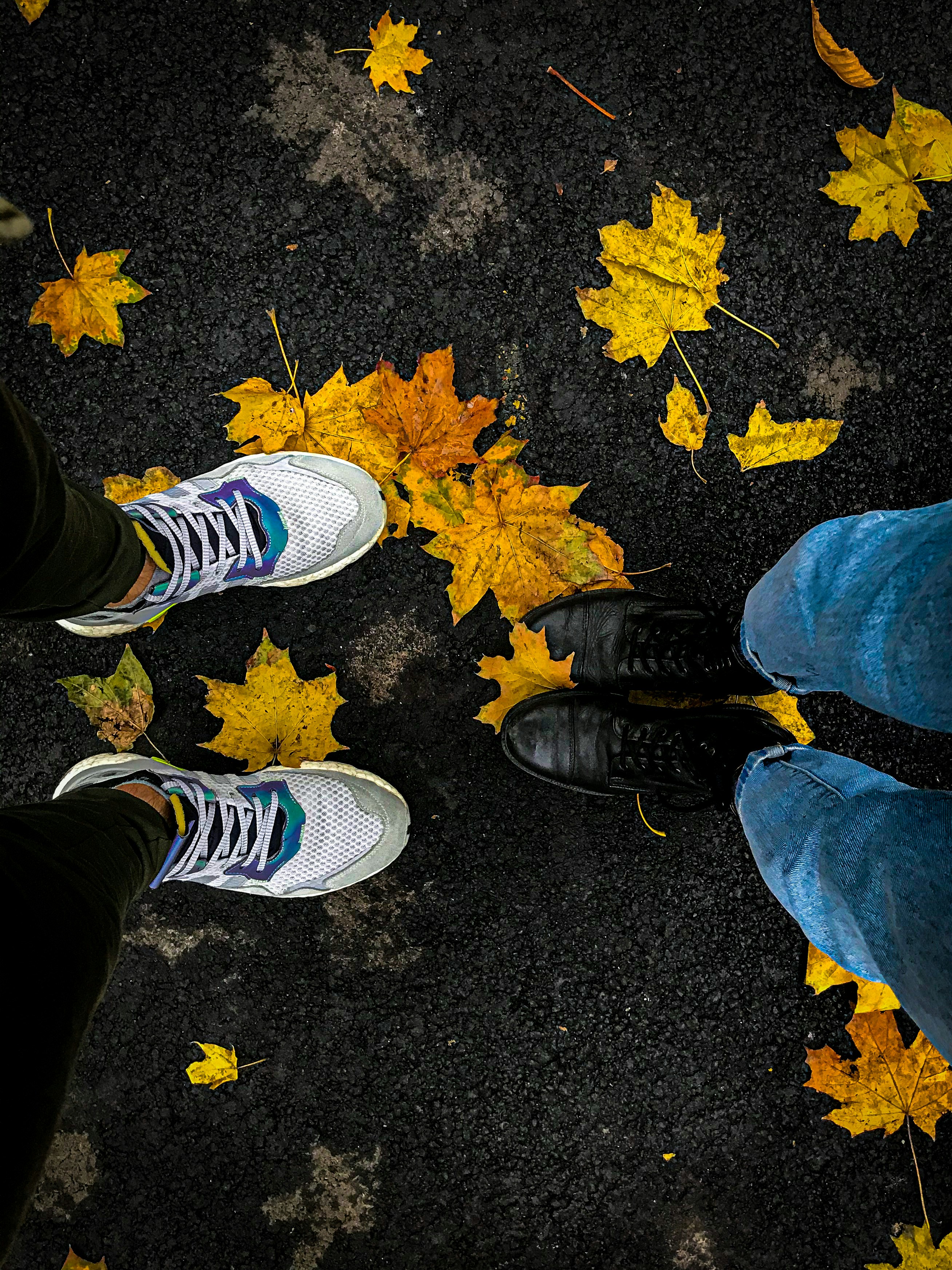 Two pairs of shoes stand on a path covered with vibrant autumn leaves, capturing the essence of the season.
