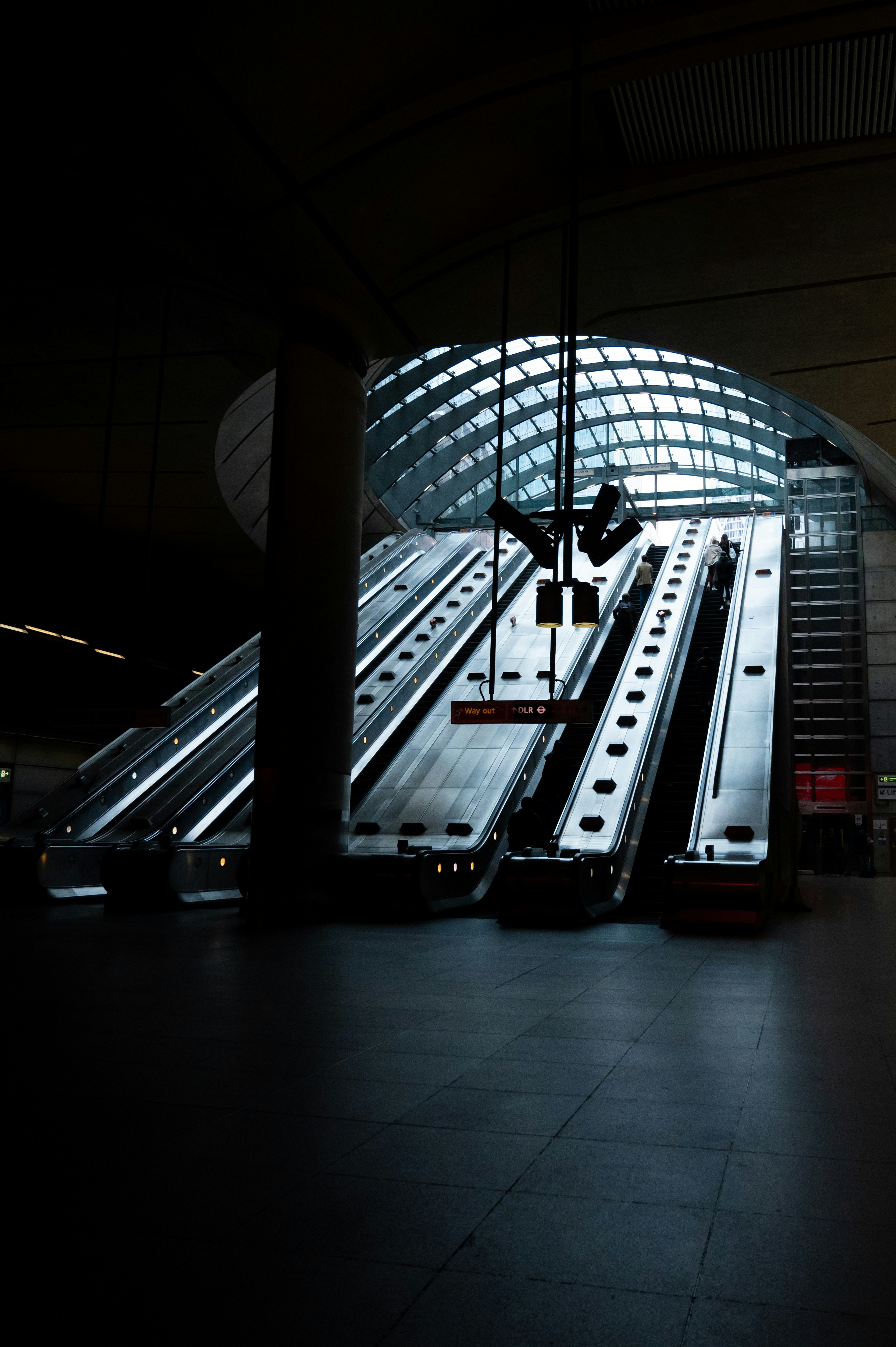 Modern escalators leading upward in a dimly lit metro station, framed by a striking glass ceiling.