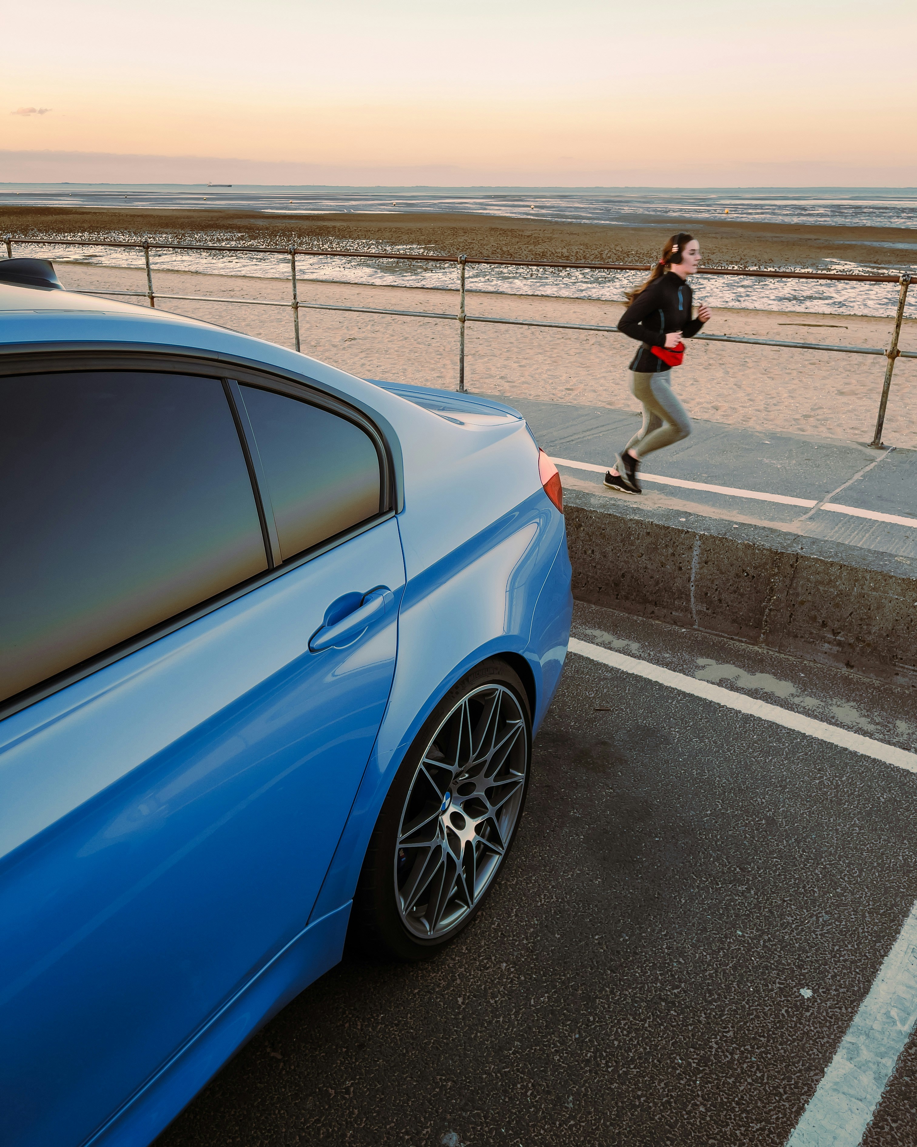 Blue sedan at the seaside: a runner passing the promenade