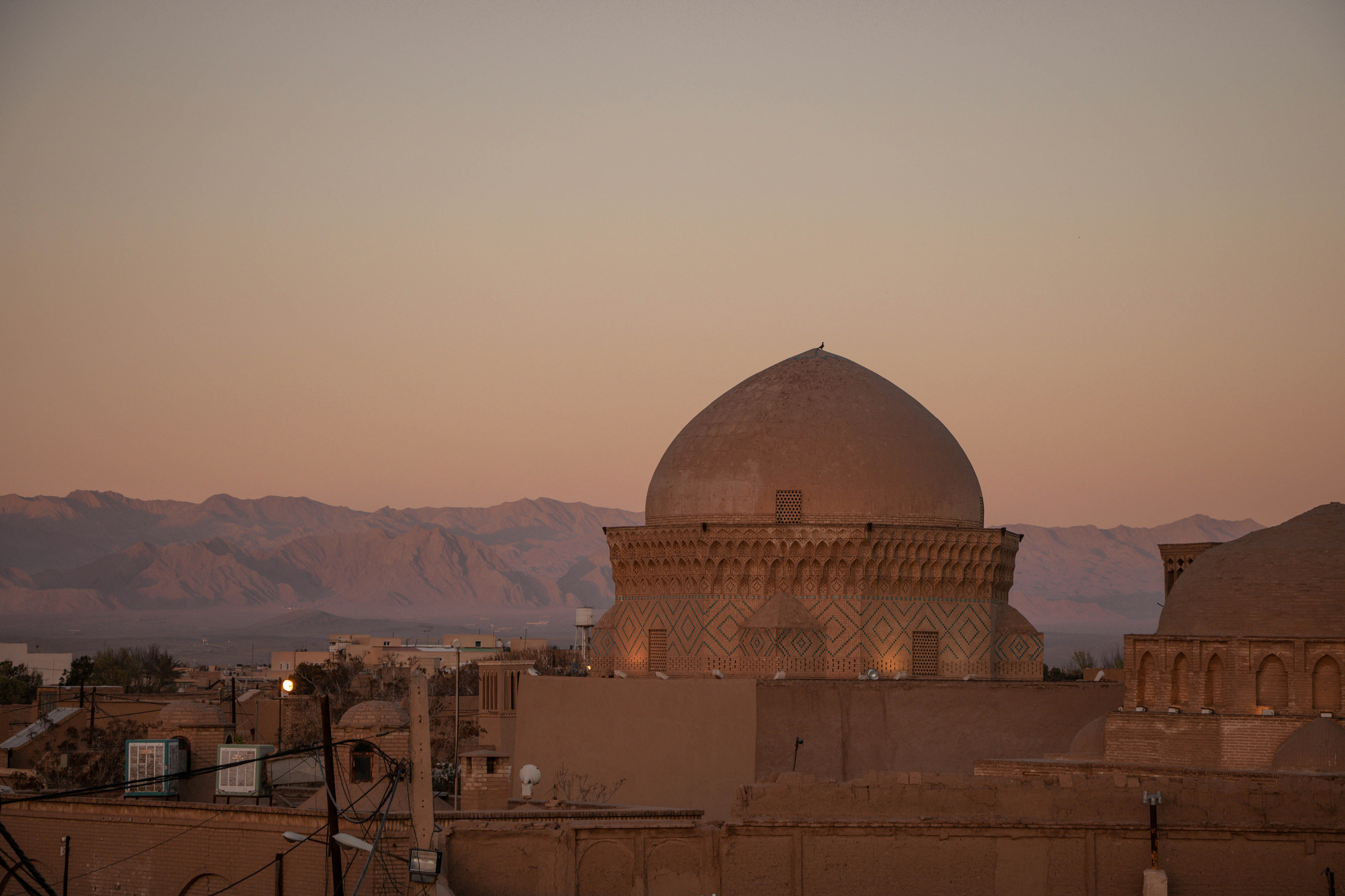 Historic dome of a mosque silhouetted against a twilight sky, with distant mountains providing a serene backdrop.