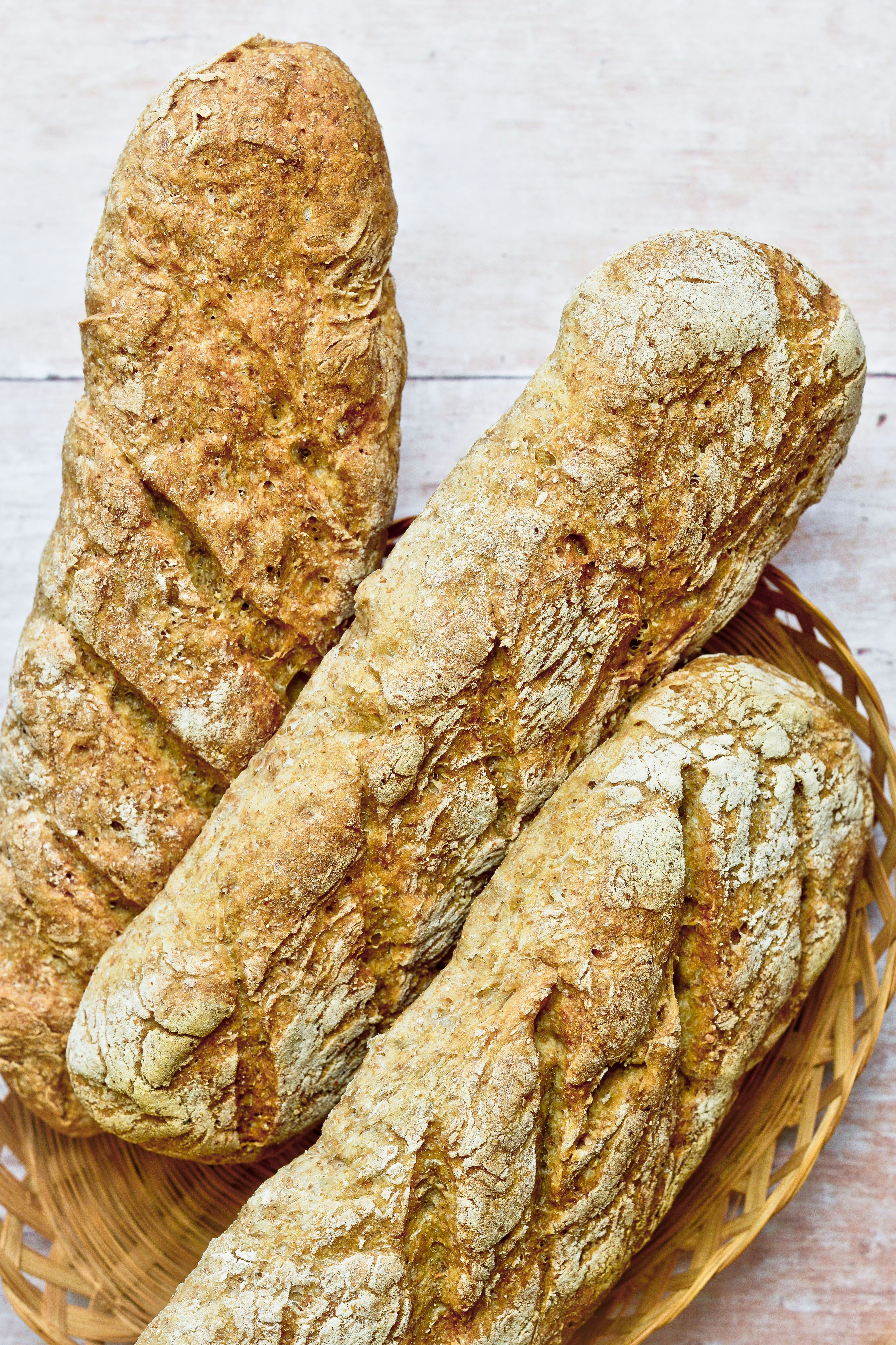 Three rustic artisan bread loaves arranged in a woven basket, showcasing their crusty texture and golden hues.