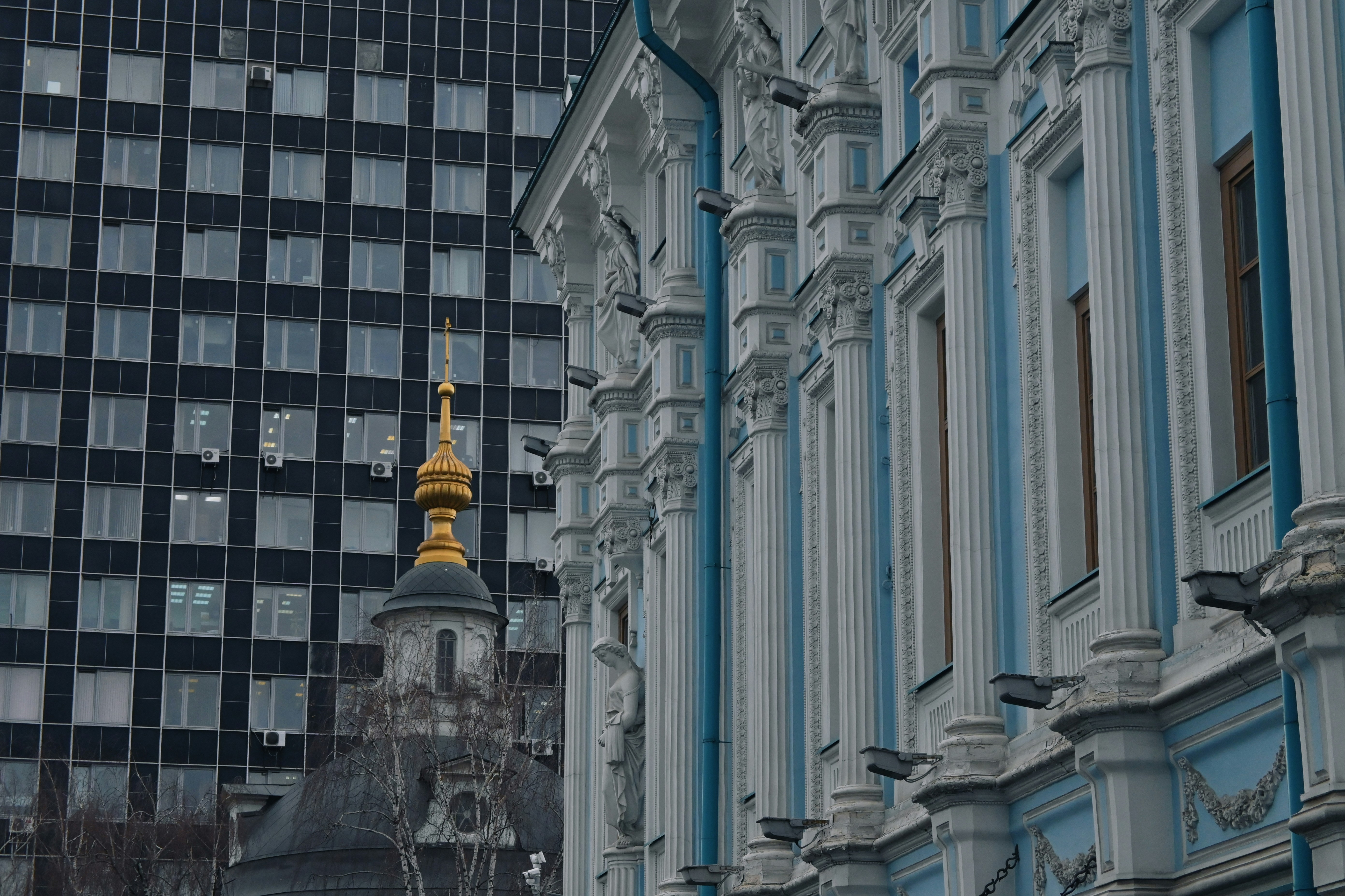 Ornate classical facade contrasts with modern glass building under cloudy skies.