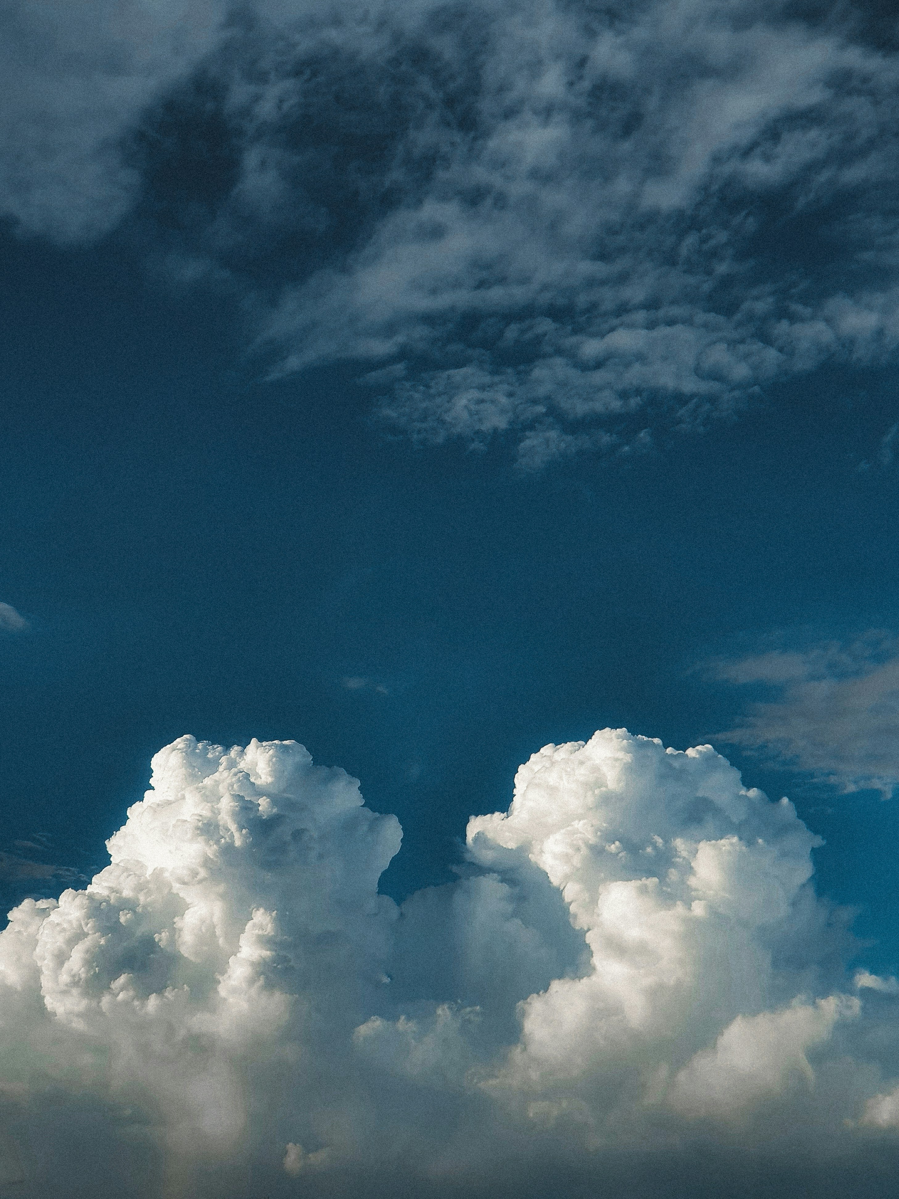 Fluffy white clouds billow against a deep blue sky, creating a serene and expansive atmosphere. The interplay of light and shadow enhances their texture.