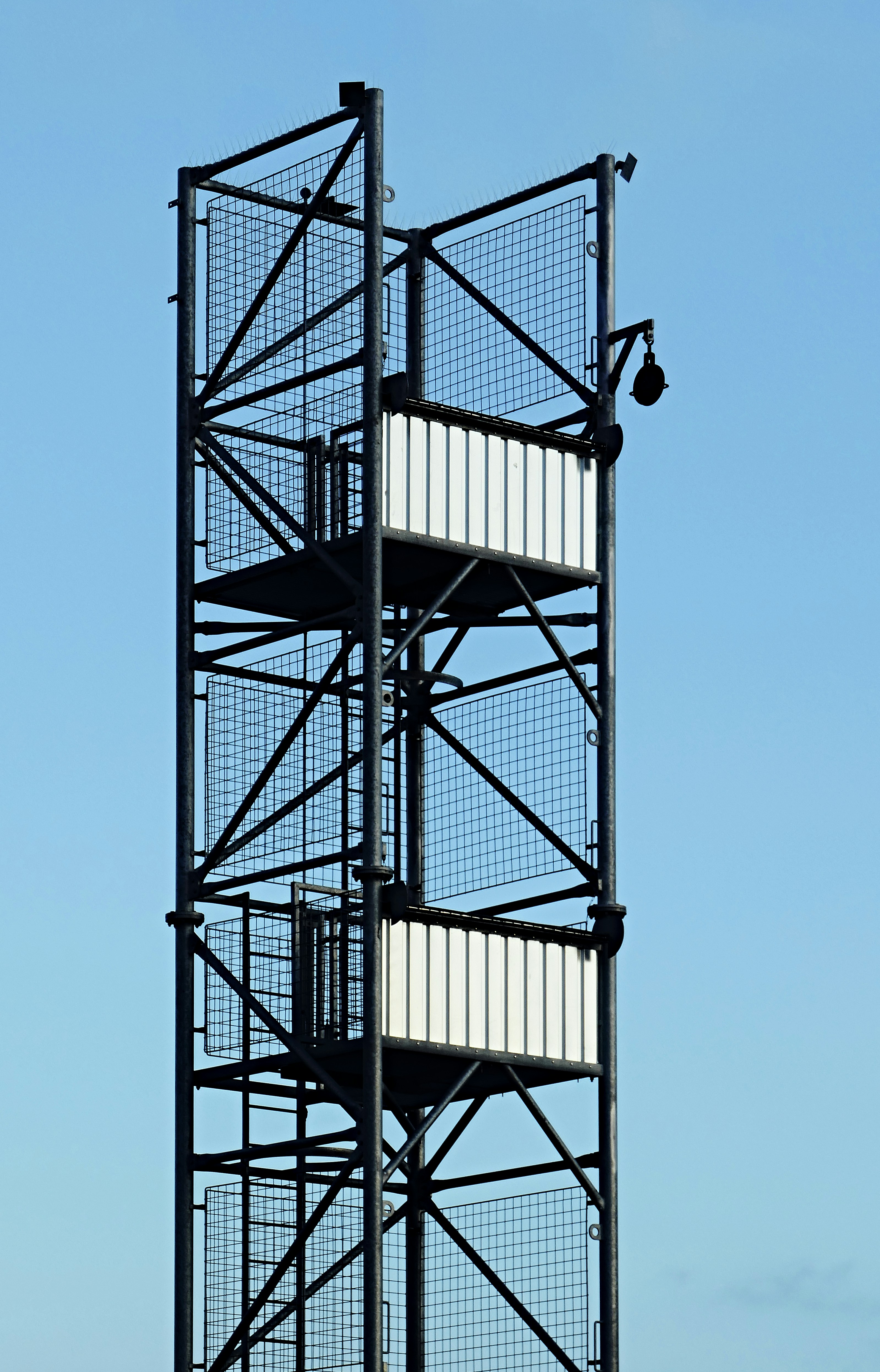 A tall, metallic observation tower featuring open platforms and a stark geometric design against a clear blue sky.