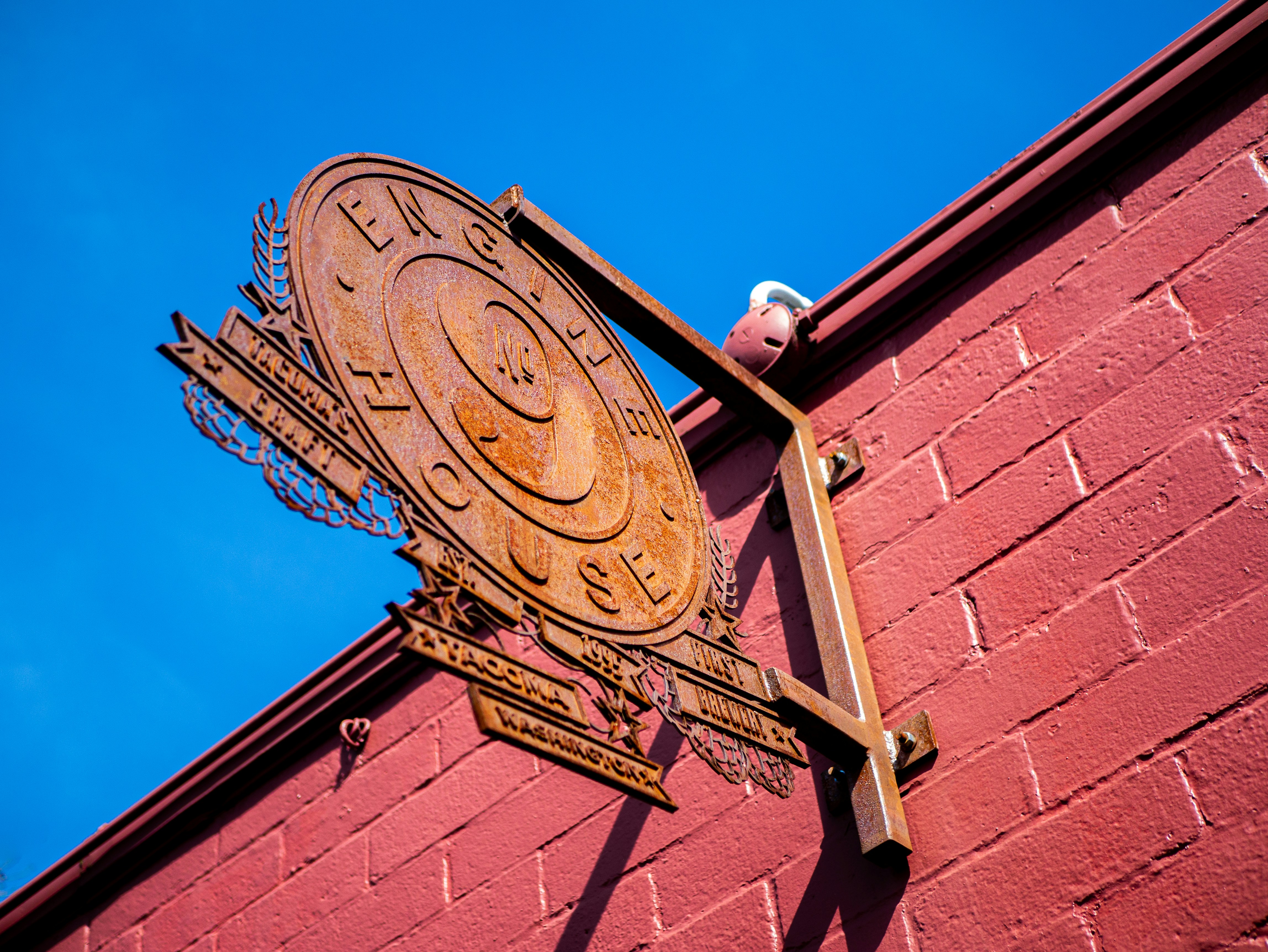 Weathered metal sign for Engine House mounted on a vibrant red wall against a clear blue sky.